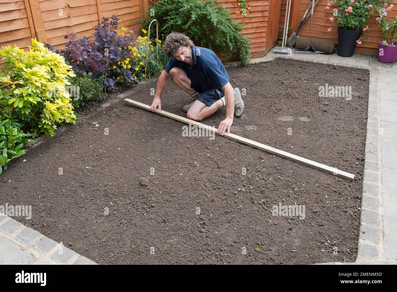Man using a wooden rule to check soil is level in preparation for ...