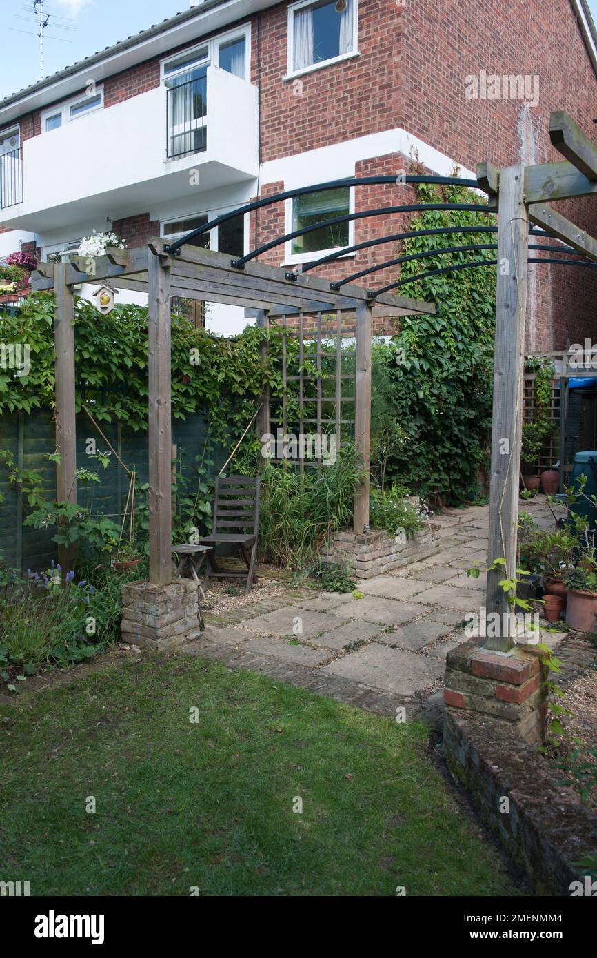 Small overlooked back garden with a wooden pergola and garden chairs ...