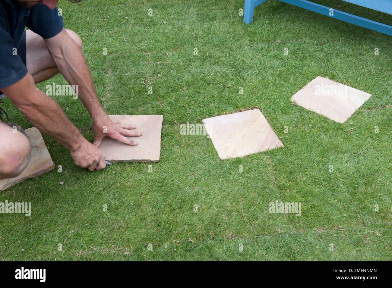 Man cutting into the turf around a paving stone to allow the slab to be ...