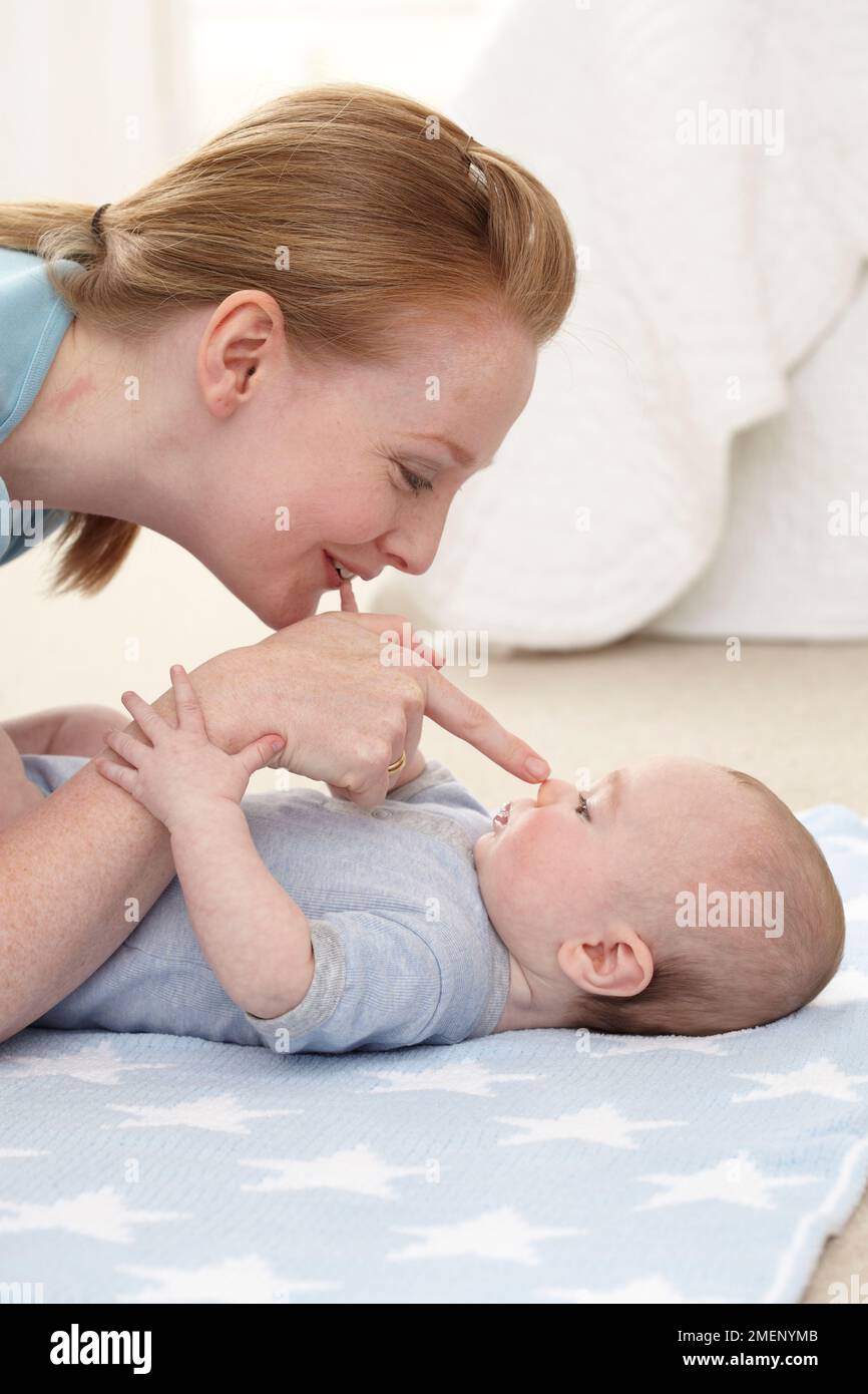 Mother touching the nose of baby boy (16 weeks) who is lying on the ...