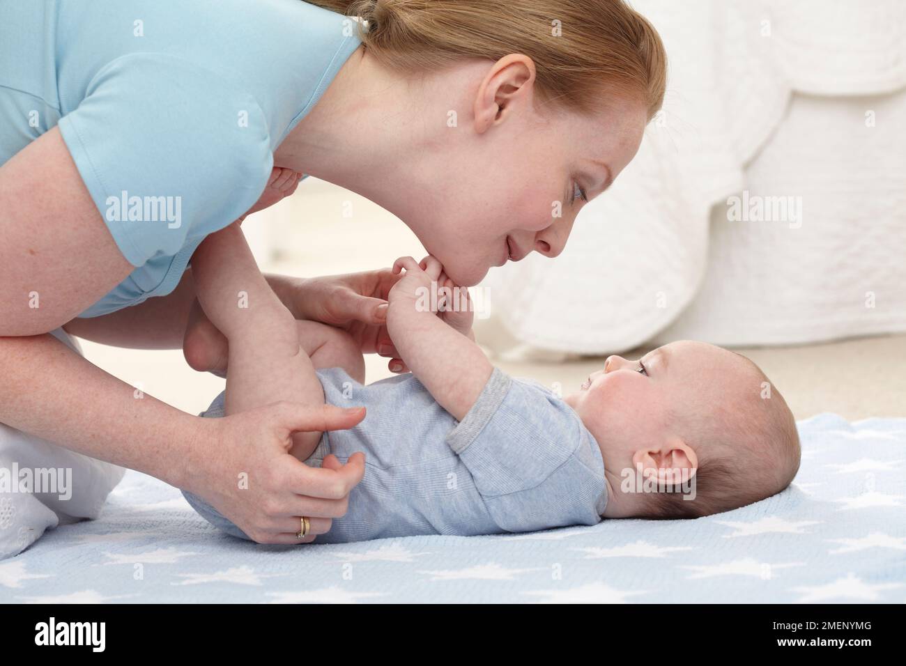 Mother kneeling over baby boy (16 weeks) who is lying on the floor on ...