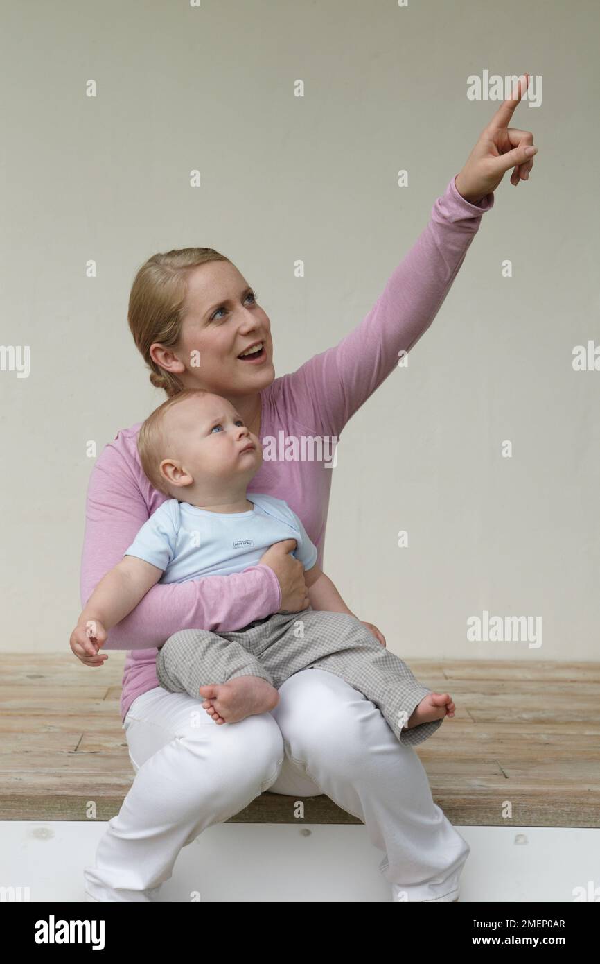 Mother pointing upwards as she sits with baby boy (10 months) on her ...