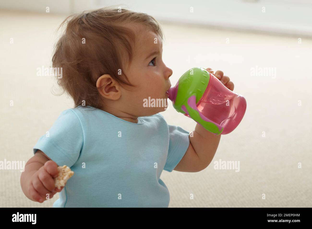 Baby girl sitting on carpet drinking from sippy cup, side view, (11.5 ...