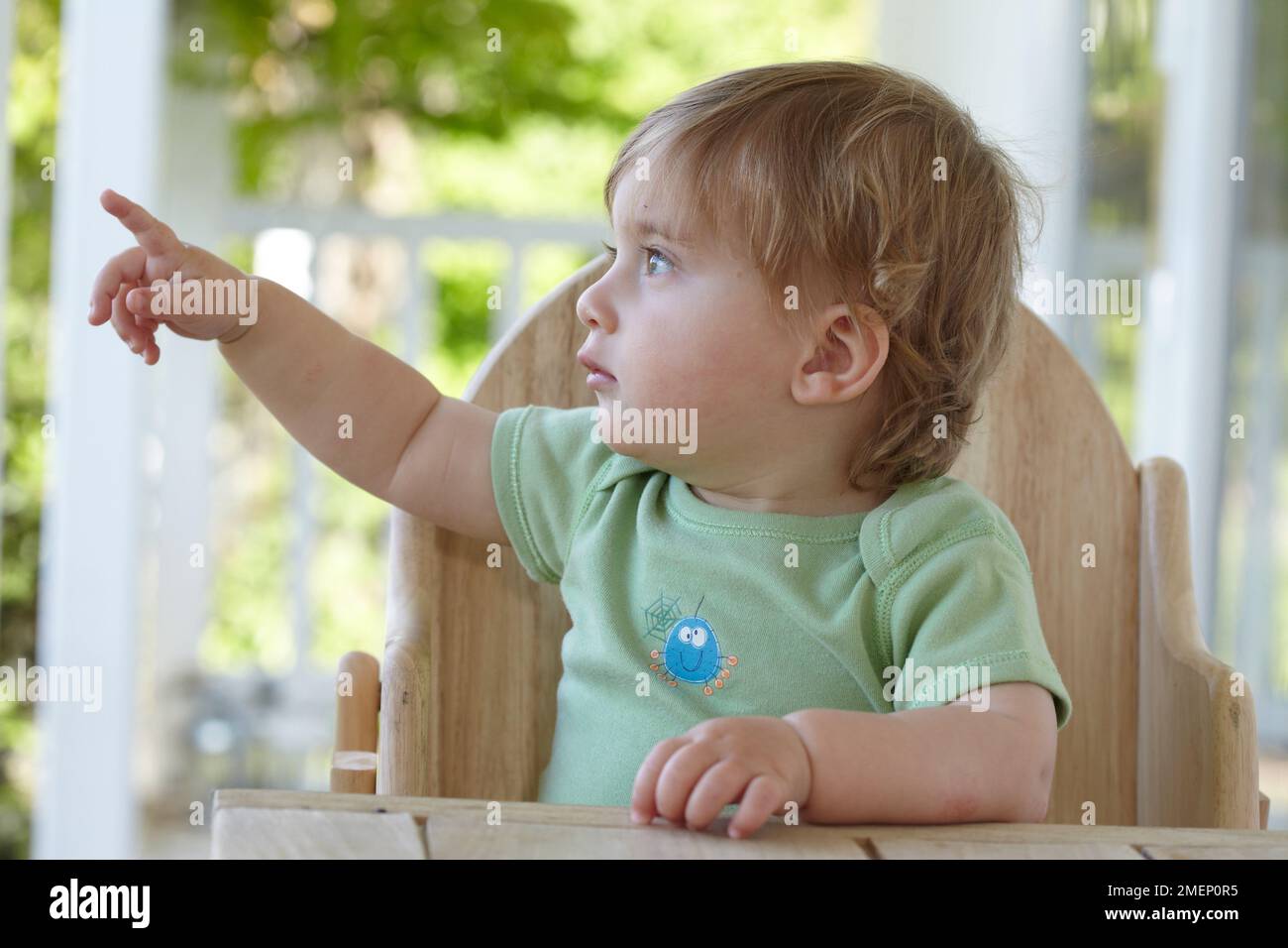 Baby boy (11.5 months) sitting in highchair with arm up and pointing ...