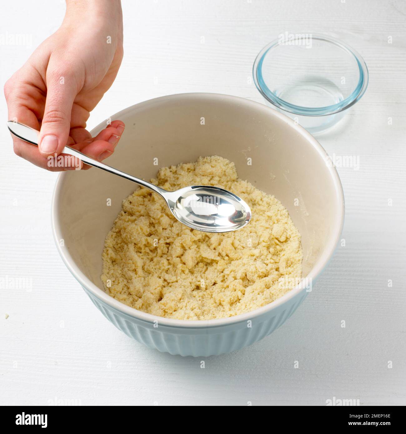 Adding tablespoon of water to shortcrust pastry in mixing bowl, close ...