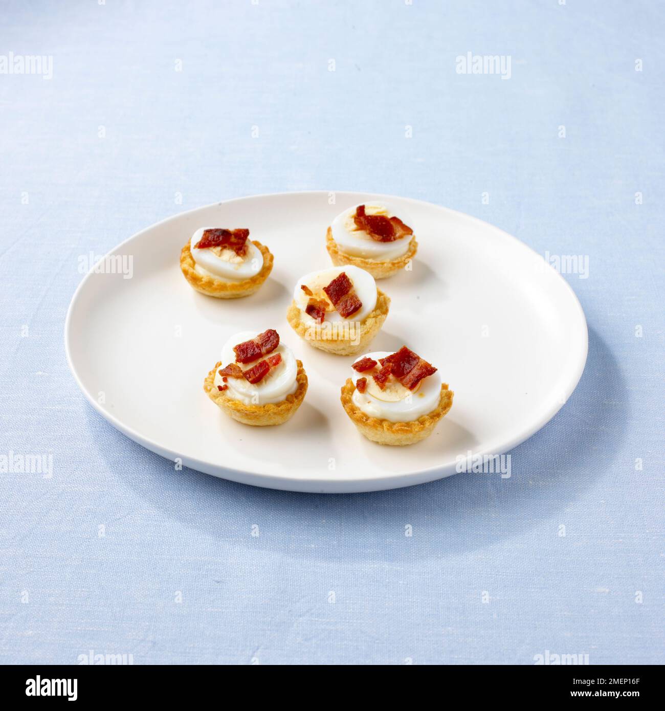 Hard boiled egg and fried bacon croustade canapes on large white plate ...