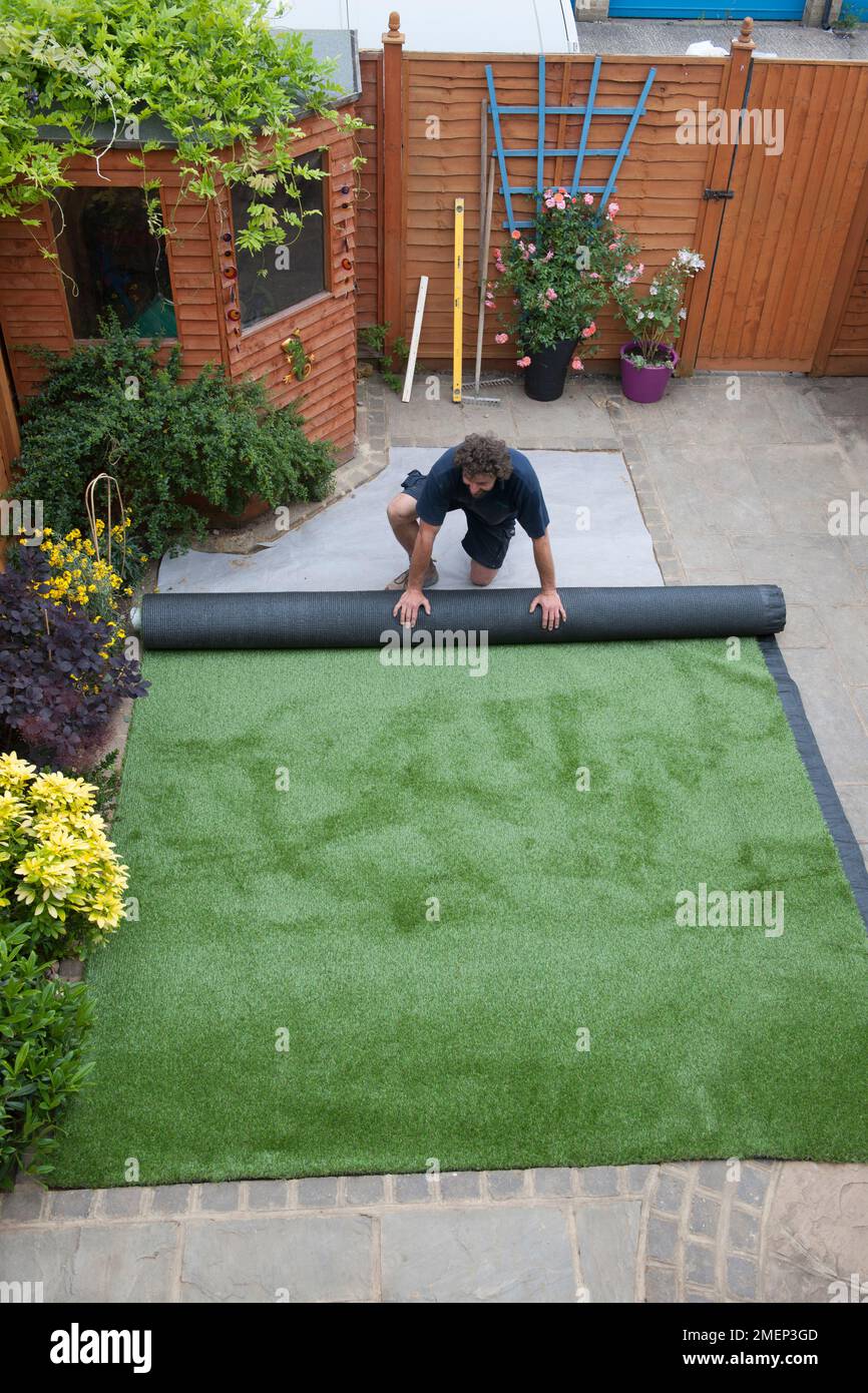 Man rolling out artificial turf in small garden, aerial view Stock ...