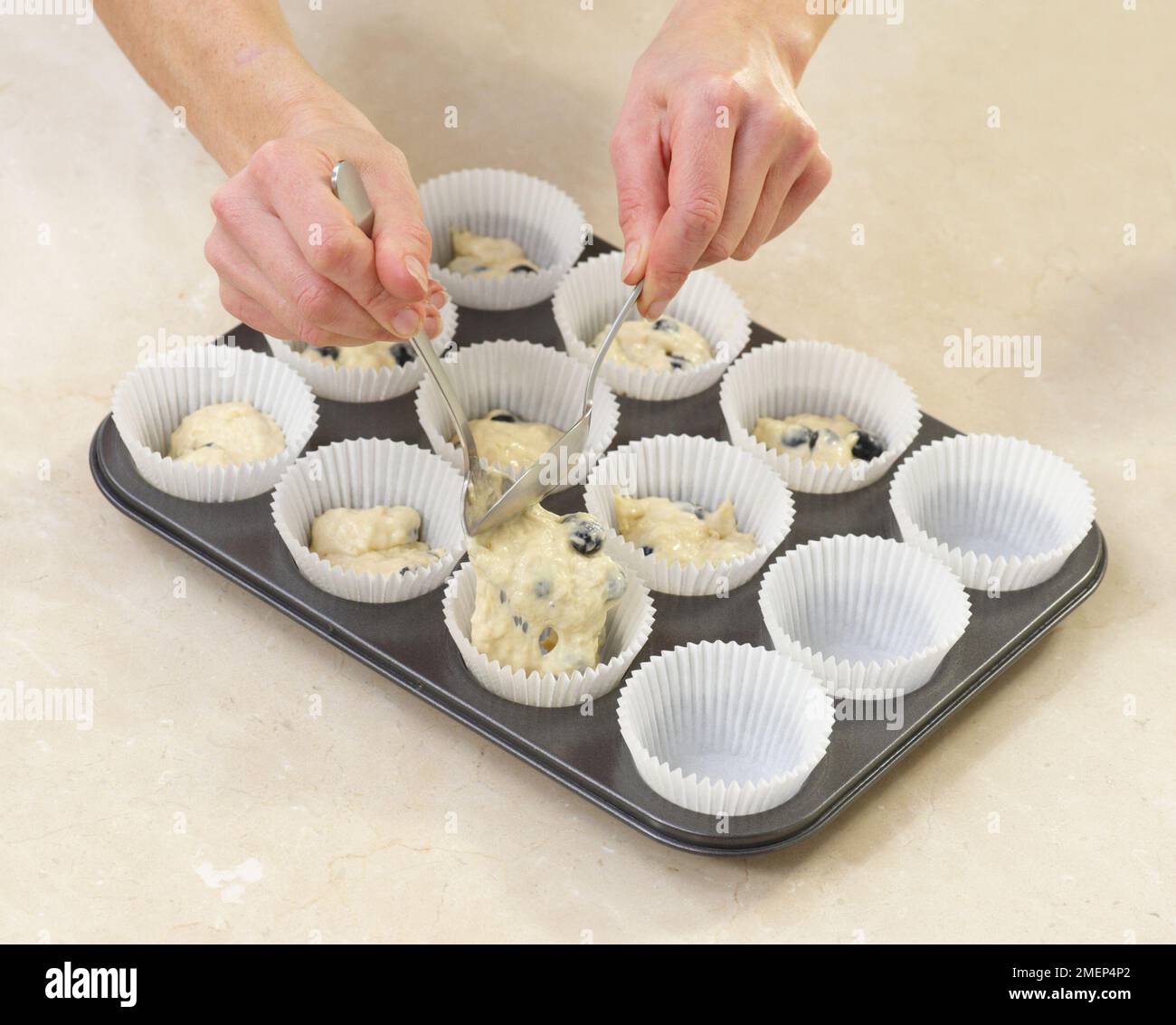 Making Lemon and Blueberry Muffins, spooning mixture into cake cases ...