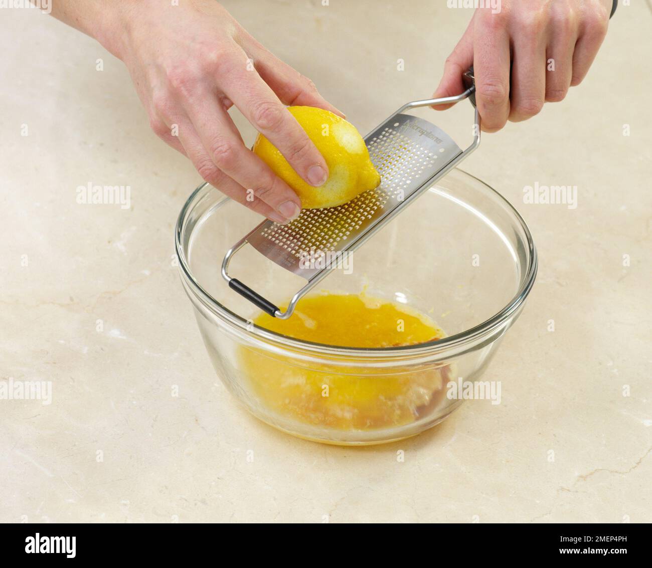 Grating lemon zest into bowl containing sugar and lemon juice, making ...