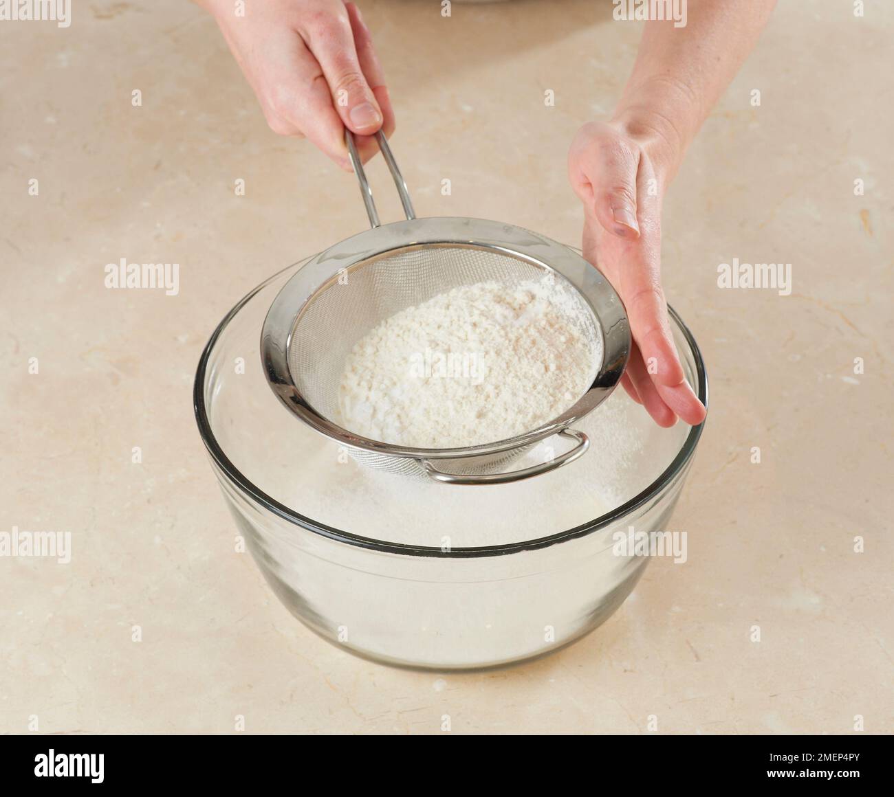Sieving flour into glass mixing bowl Stock Photo - Alamy