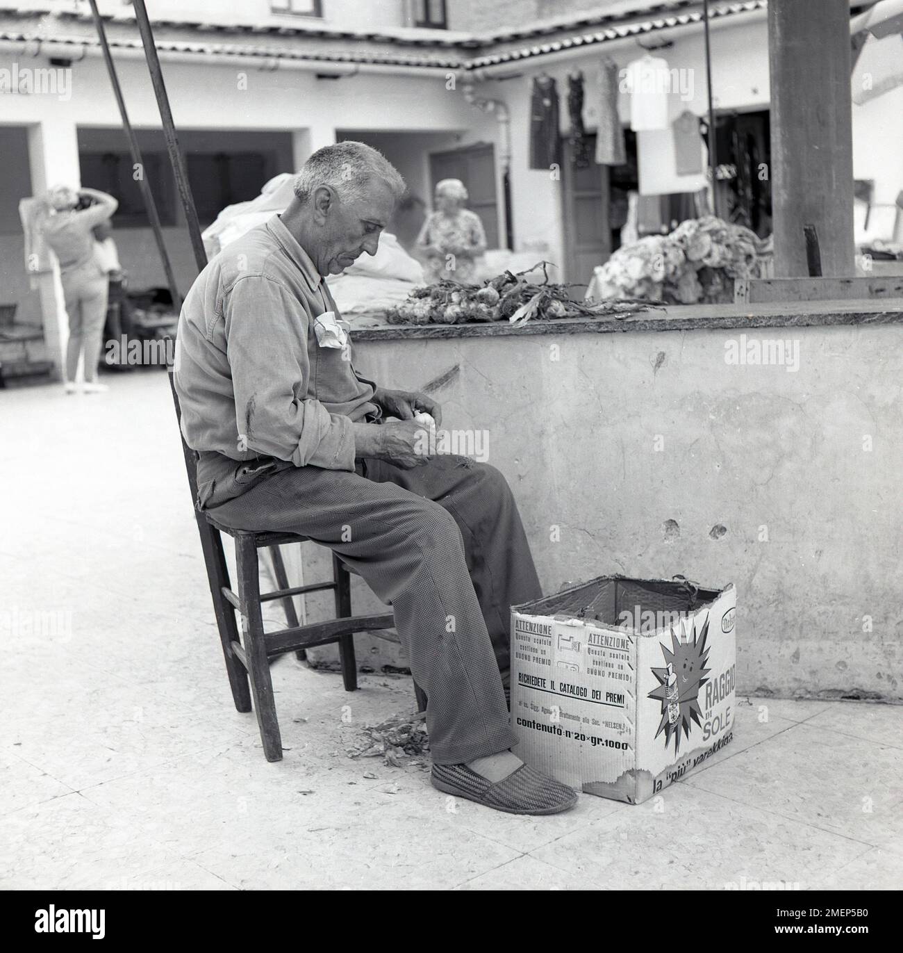 1960s, historical, sitting on a wooden chair outside on a town square ...