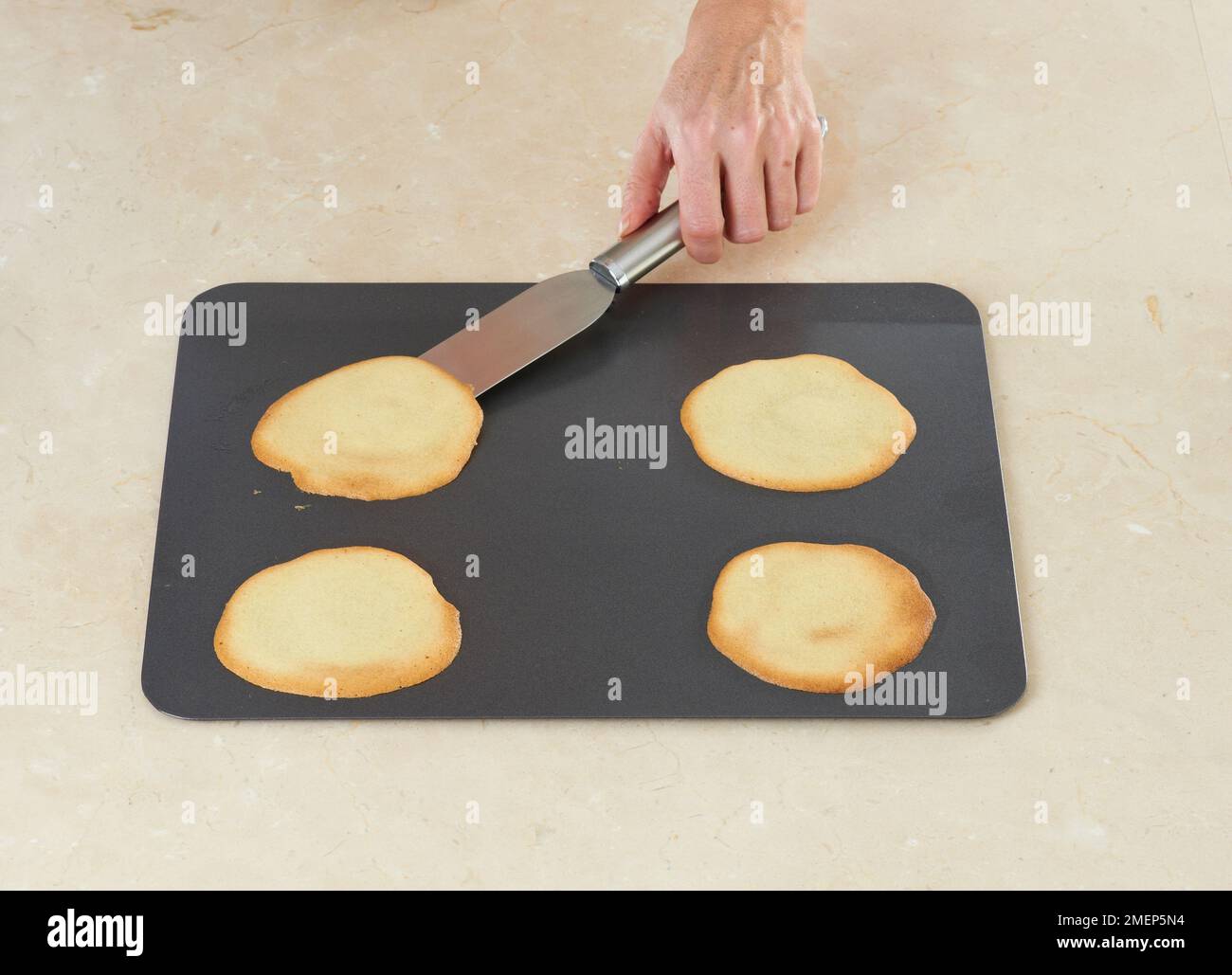 Removing baked flat Tuiles from baking tray using spatula Stock Photo ...