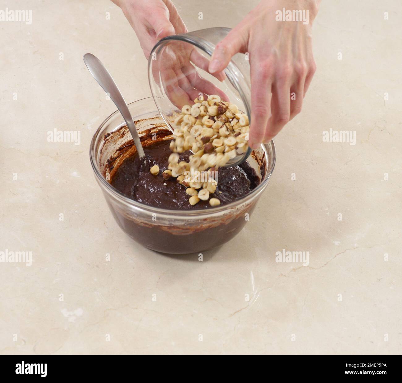Making Chocolate and Hazelnut Brownies, tipping chopped nuts into ...