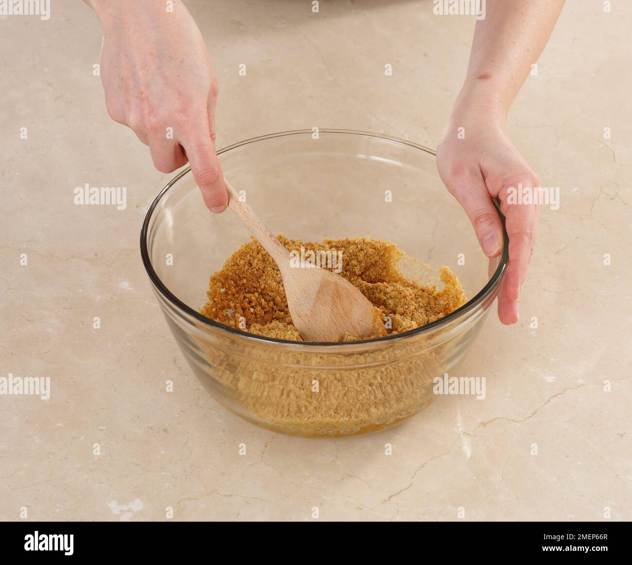 Mixing melted butter with crushed biscuits, to make biscuit base for ...