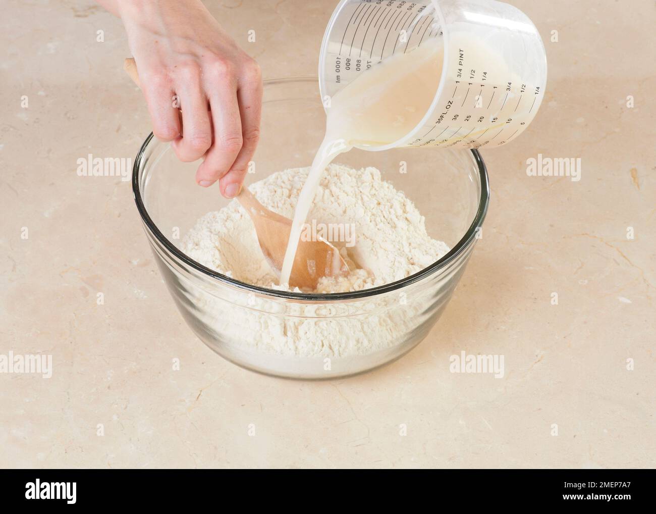Pouring yeast and water into flour and stir in glass mixing bowl Stock ...