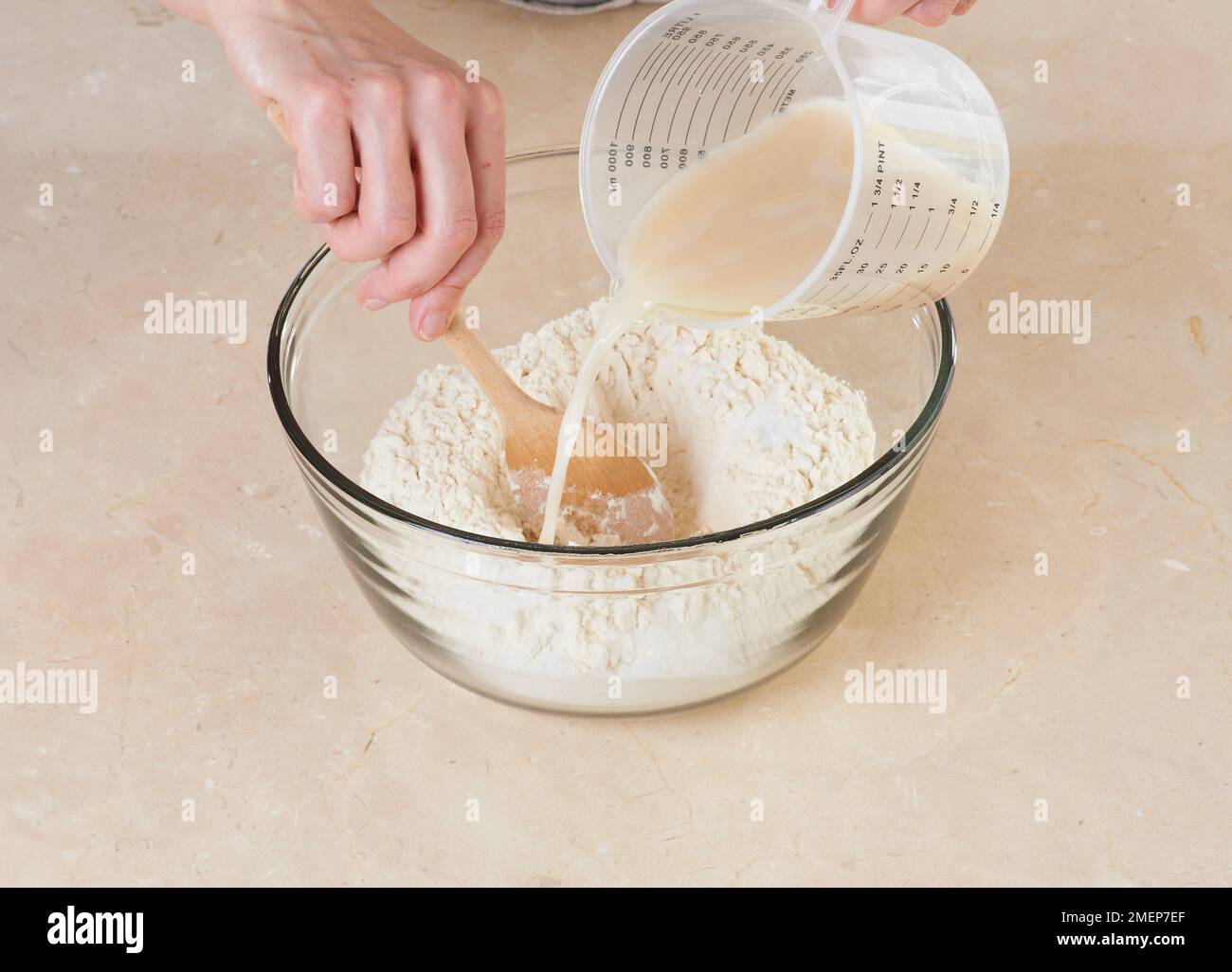 Pouring yeast from measuring jug into flour in glass mixing bowl Stock ...