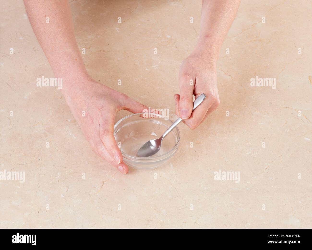 Dissolving salt in warm water using teaspoon in small glass bowl Stock ...