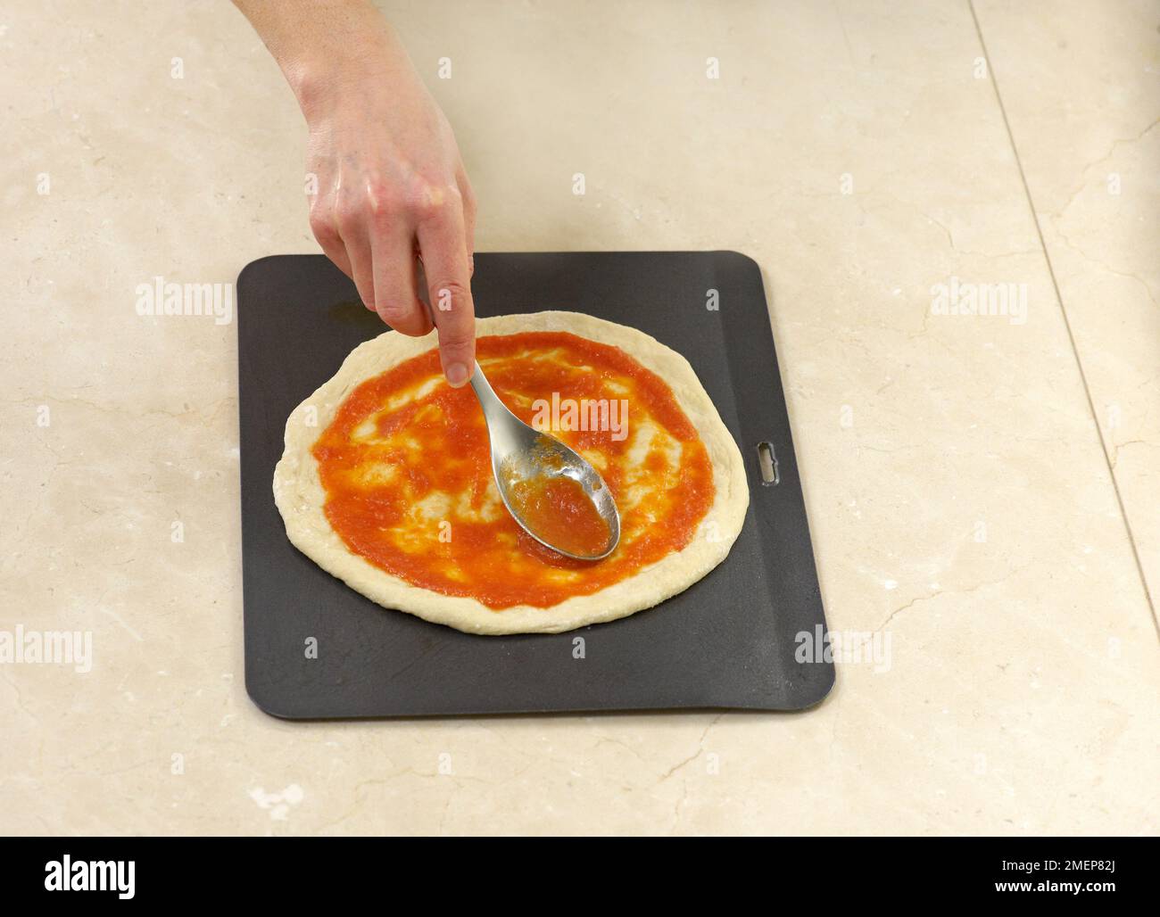 Spreading tomato sauce all over pizza base Stock Photo - Alamy