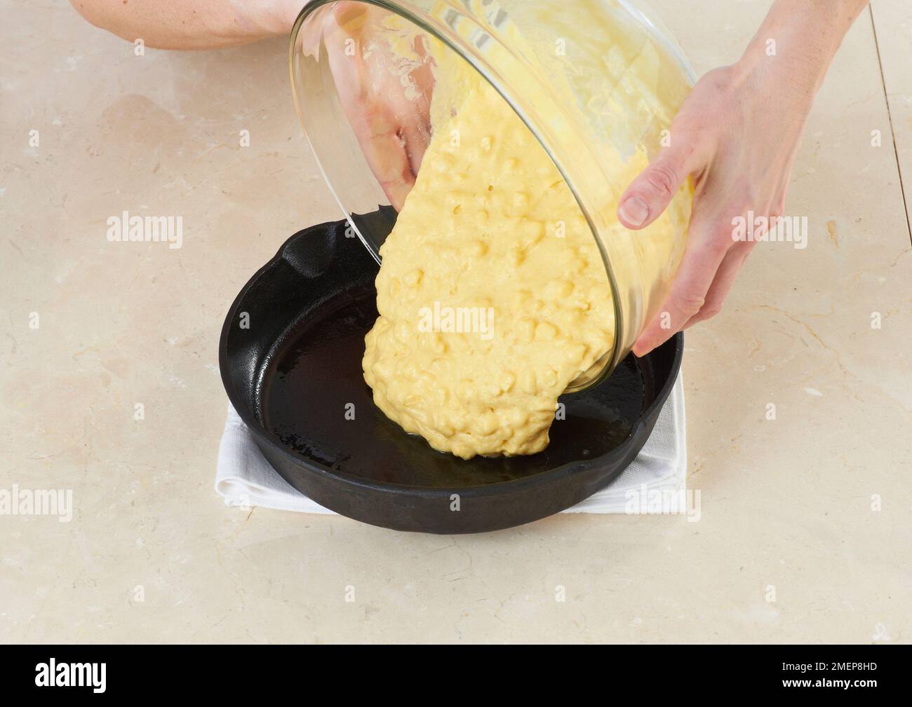 Pouring cornbread mixture into heavy frying pan on kitchen worktop ...