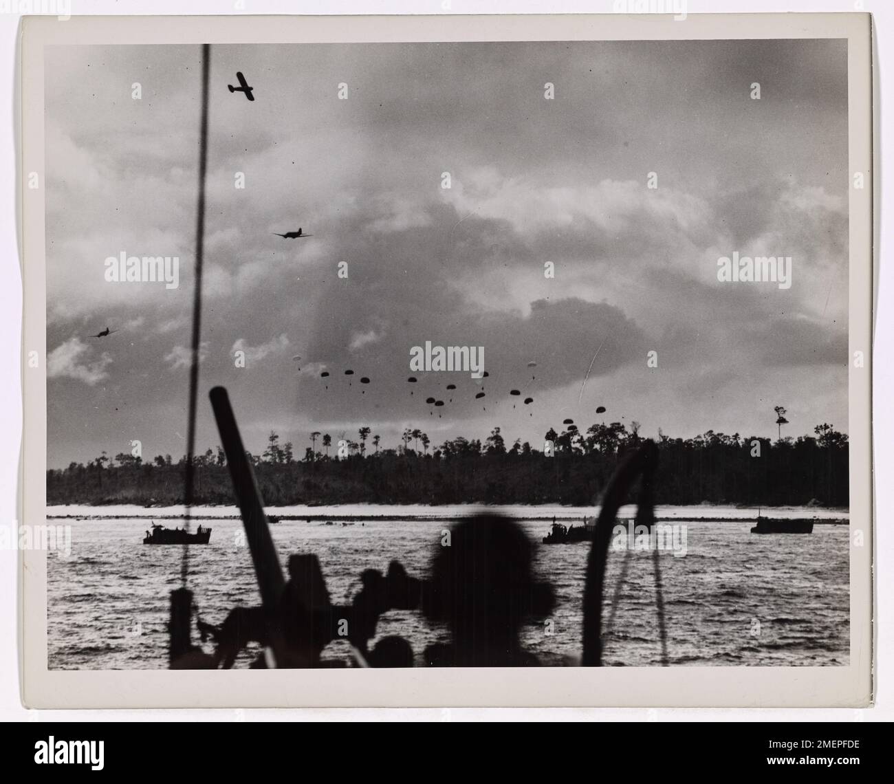 Coast Guardsmen aboard an LST watch American paratroopers jump over ...