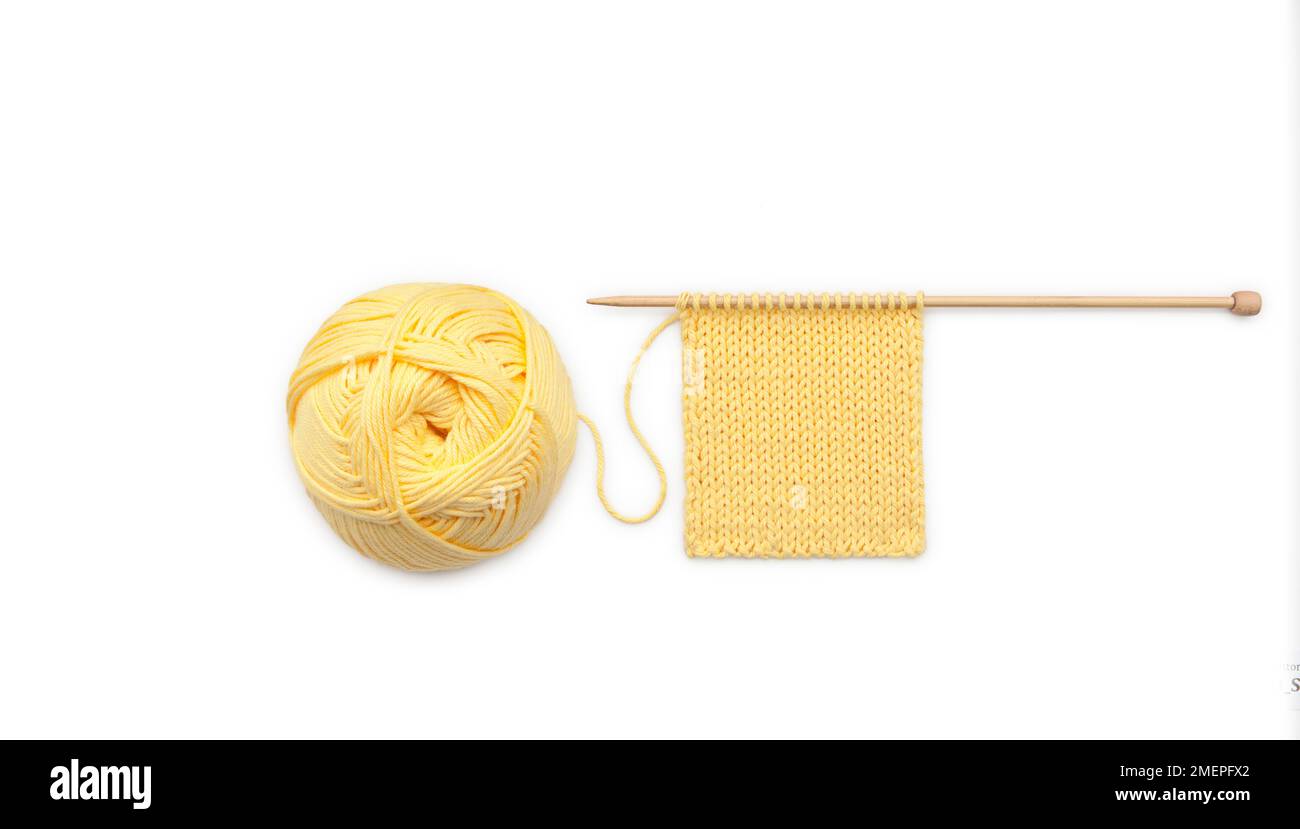 Ball of yellow matt cotton yarn and knitted sample on knitting needle ...