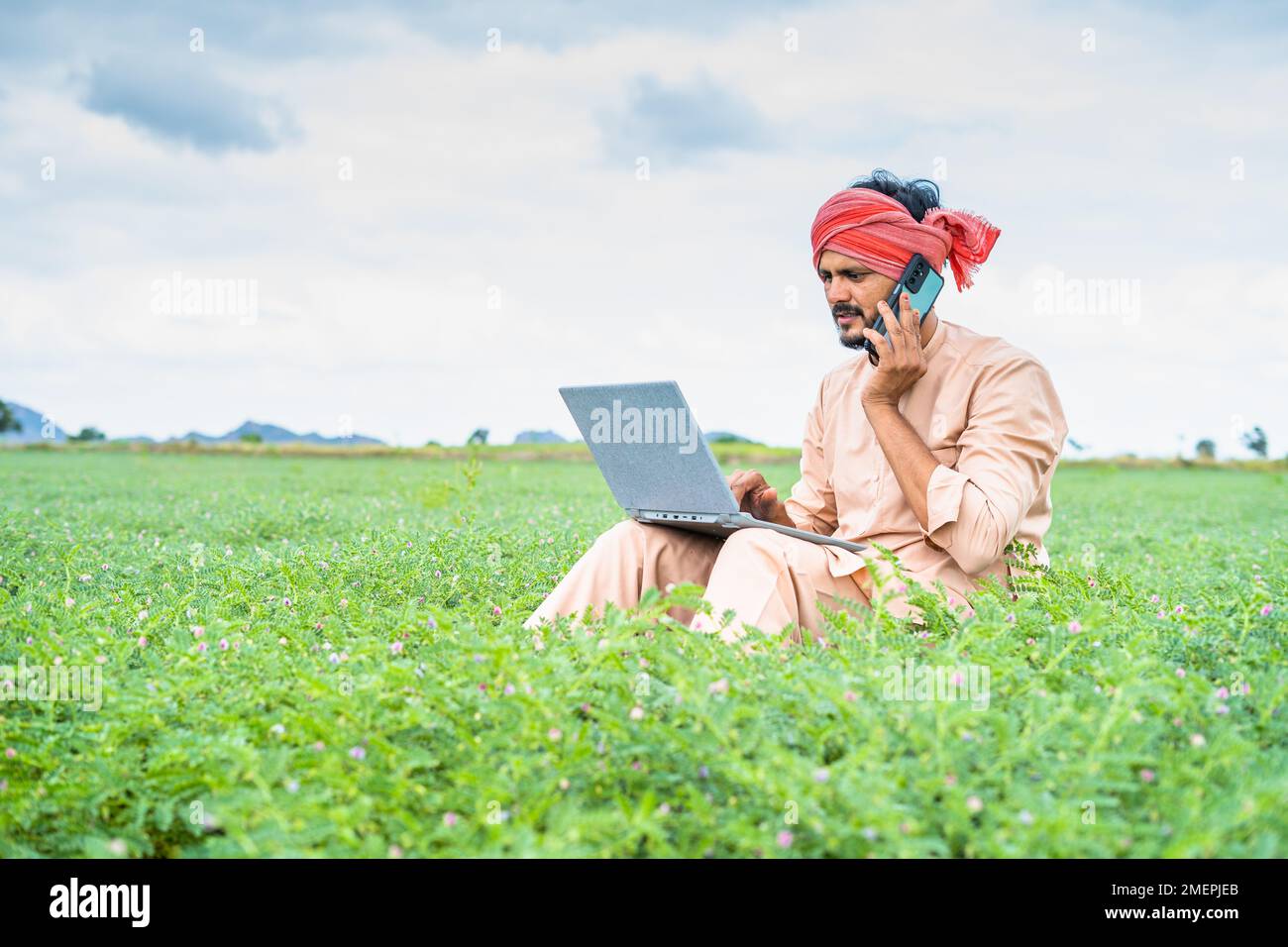 Farmer from laptop explaining on mobile phone while sitting on farmland ...