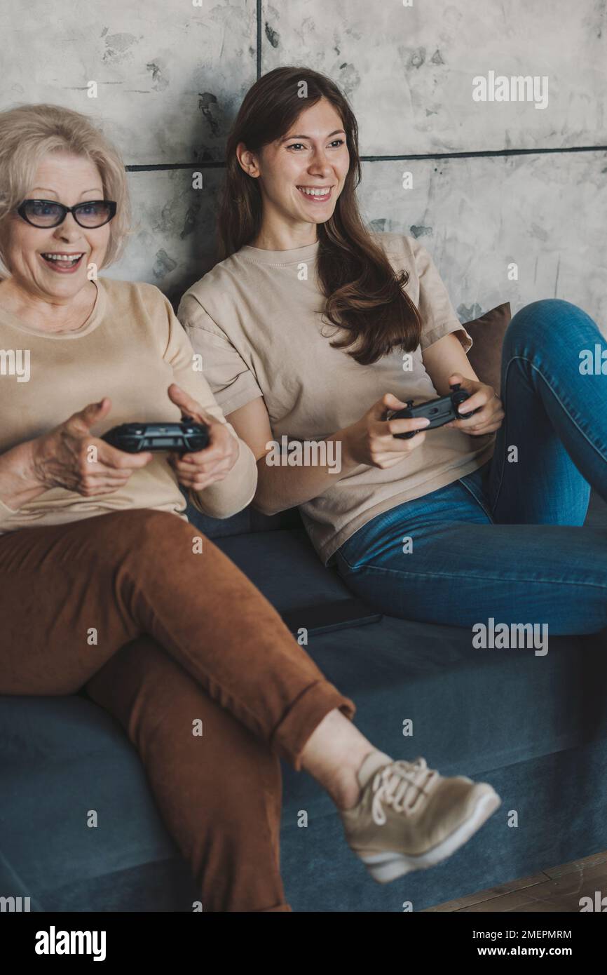 Two women playing video game together at home. Elderly mother and adult ...