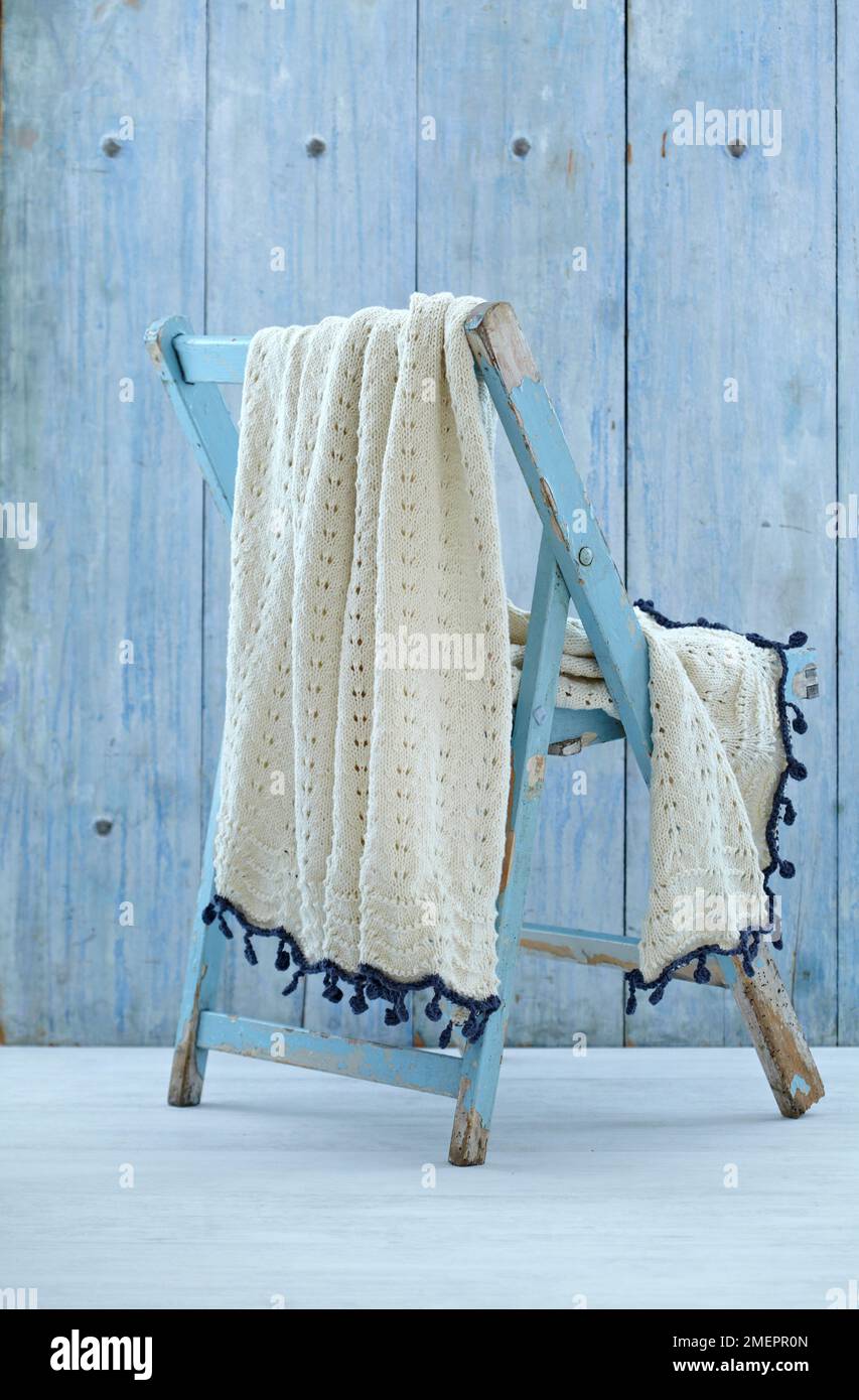 White wave-and-shell throw with blue edge, over wooden chair Stock ...
