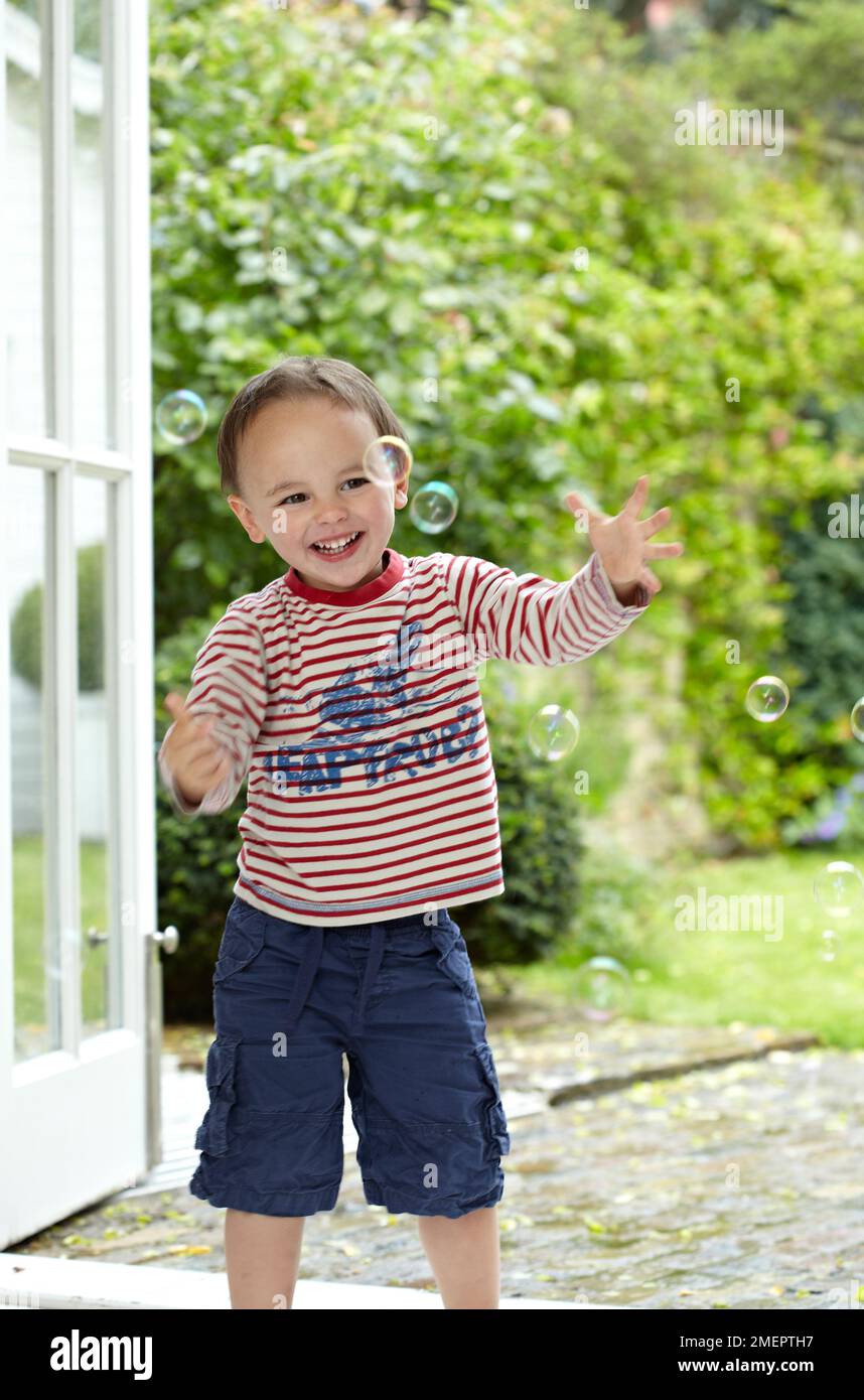 Small boy standing in doorway catching bubbles, 2 years Stock Photo - Alamy