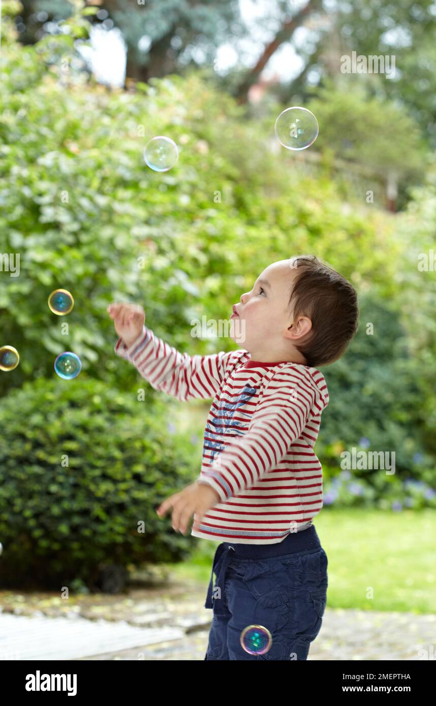 Small boy standing looking up catching bubbles, 2 years Stock Photo - Alamy