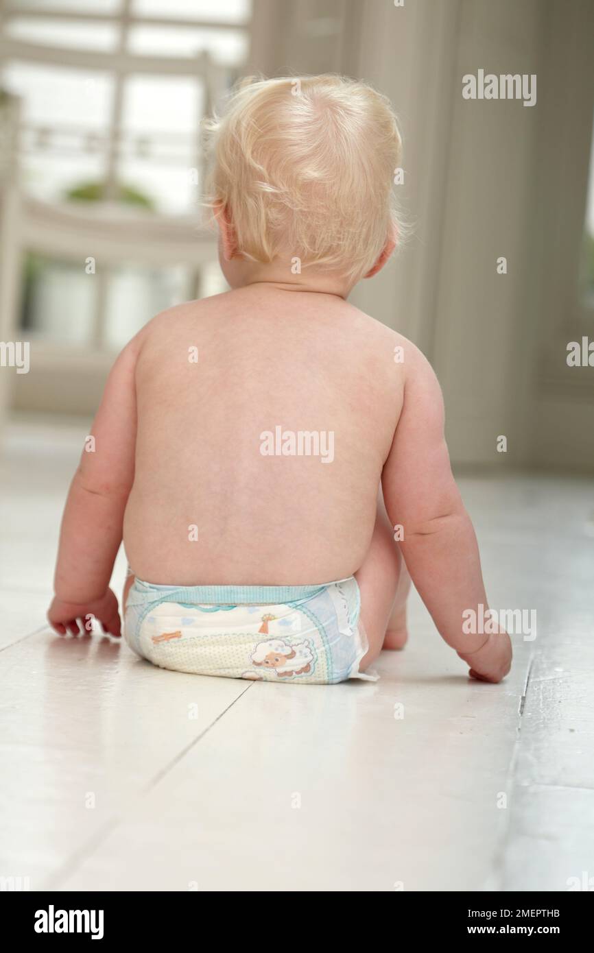 Small boy sitting on floor with back facing forward, 1 year 1 month ...