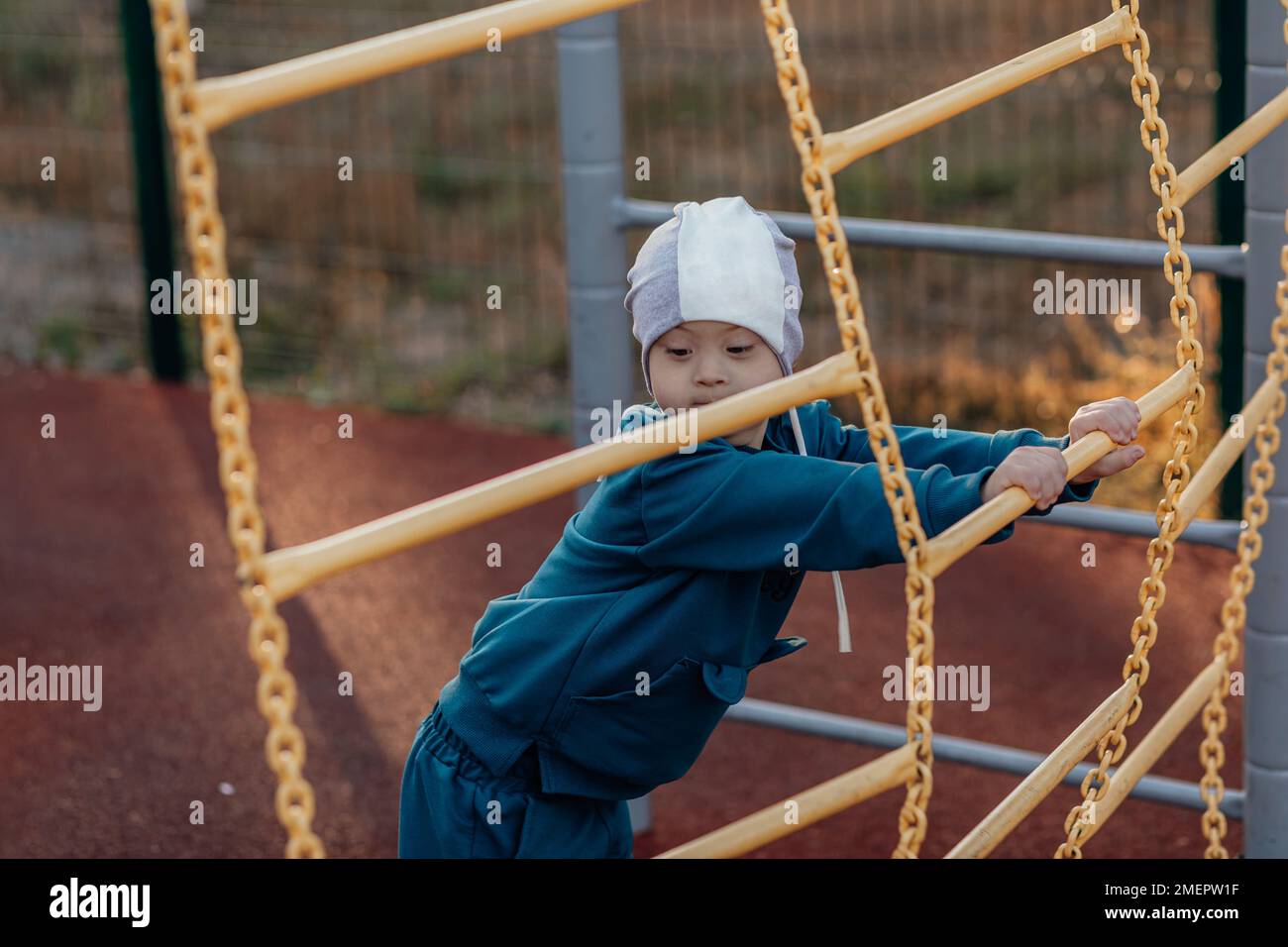 little boy with down syndrome holds onto the steps of a metal suspended ...