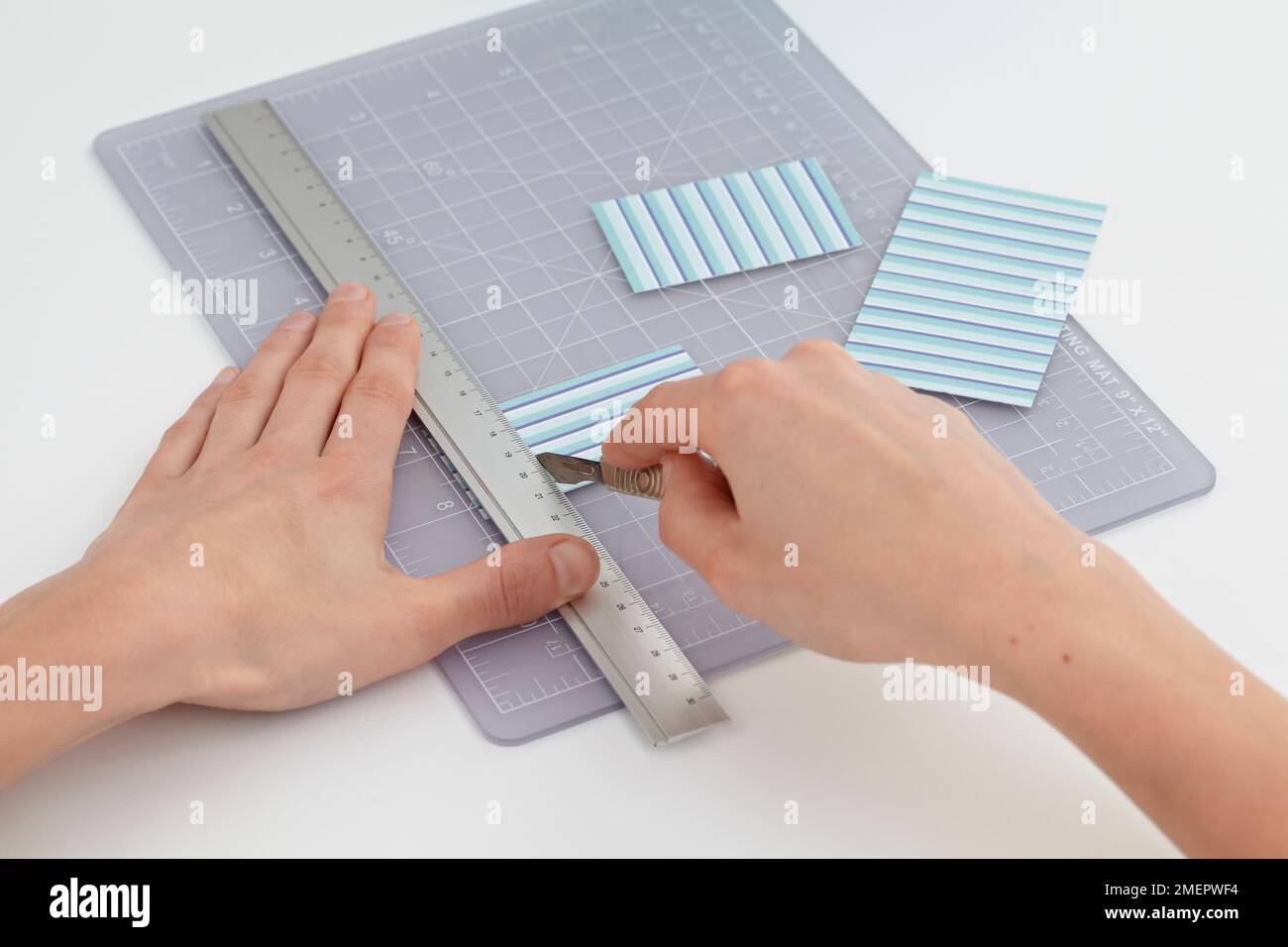 Using steel ruler and craft knife to cut striped card to make candles ...