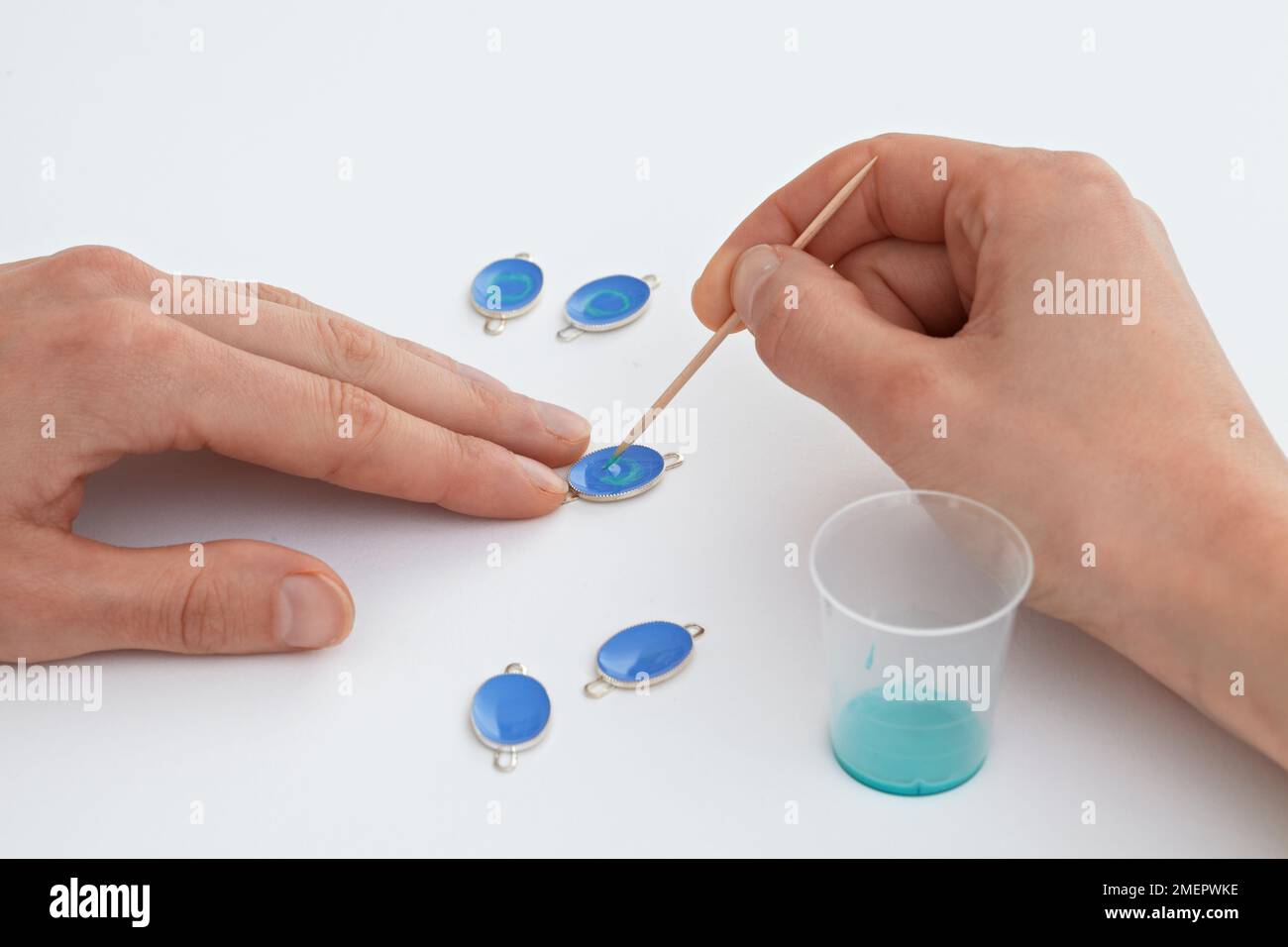 Using cocktail stick to swirl circle of mint green colour on light blue ...