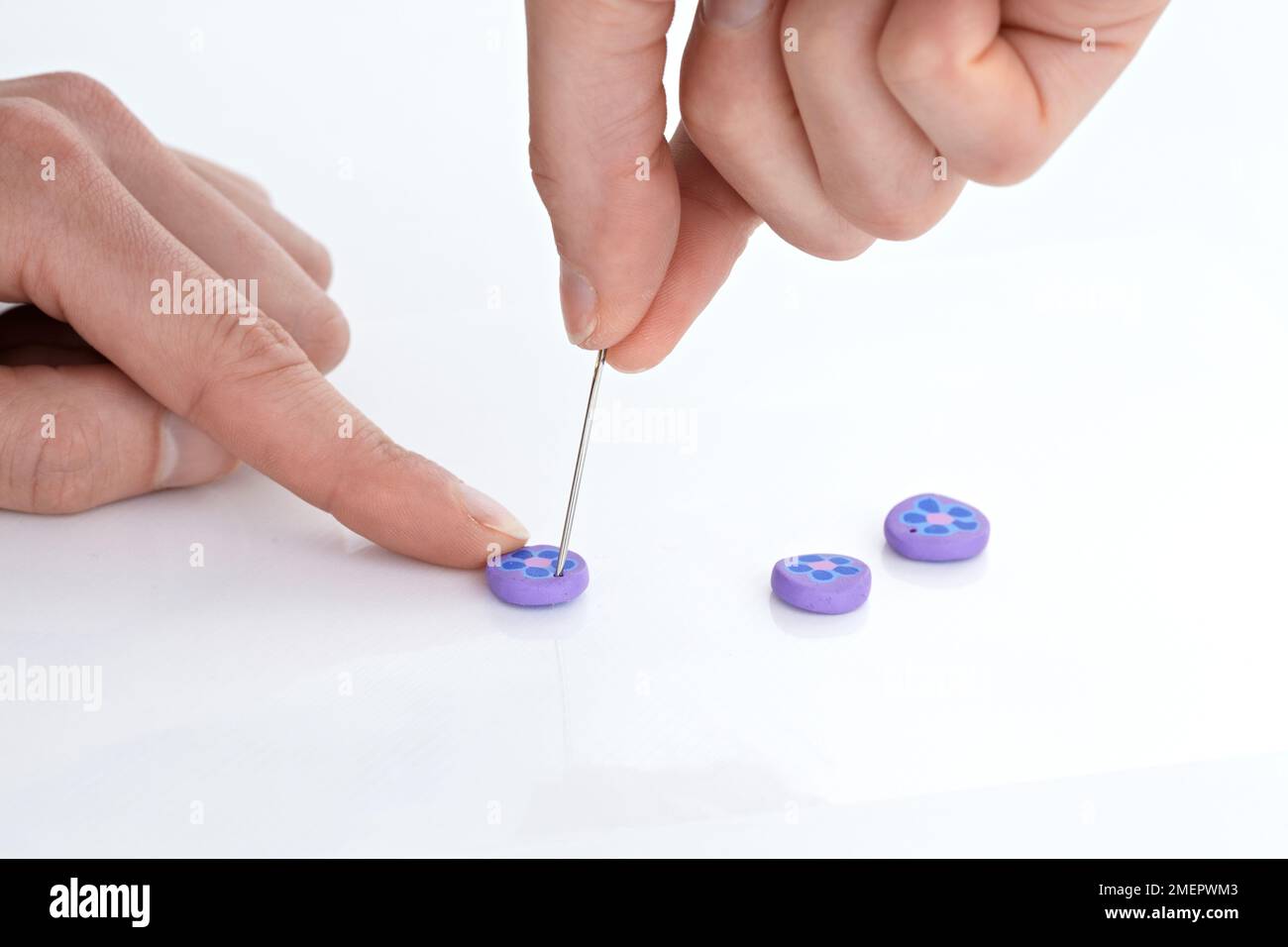 Making polymer clay pendant from canework discs, piercing hole at top ...