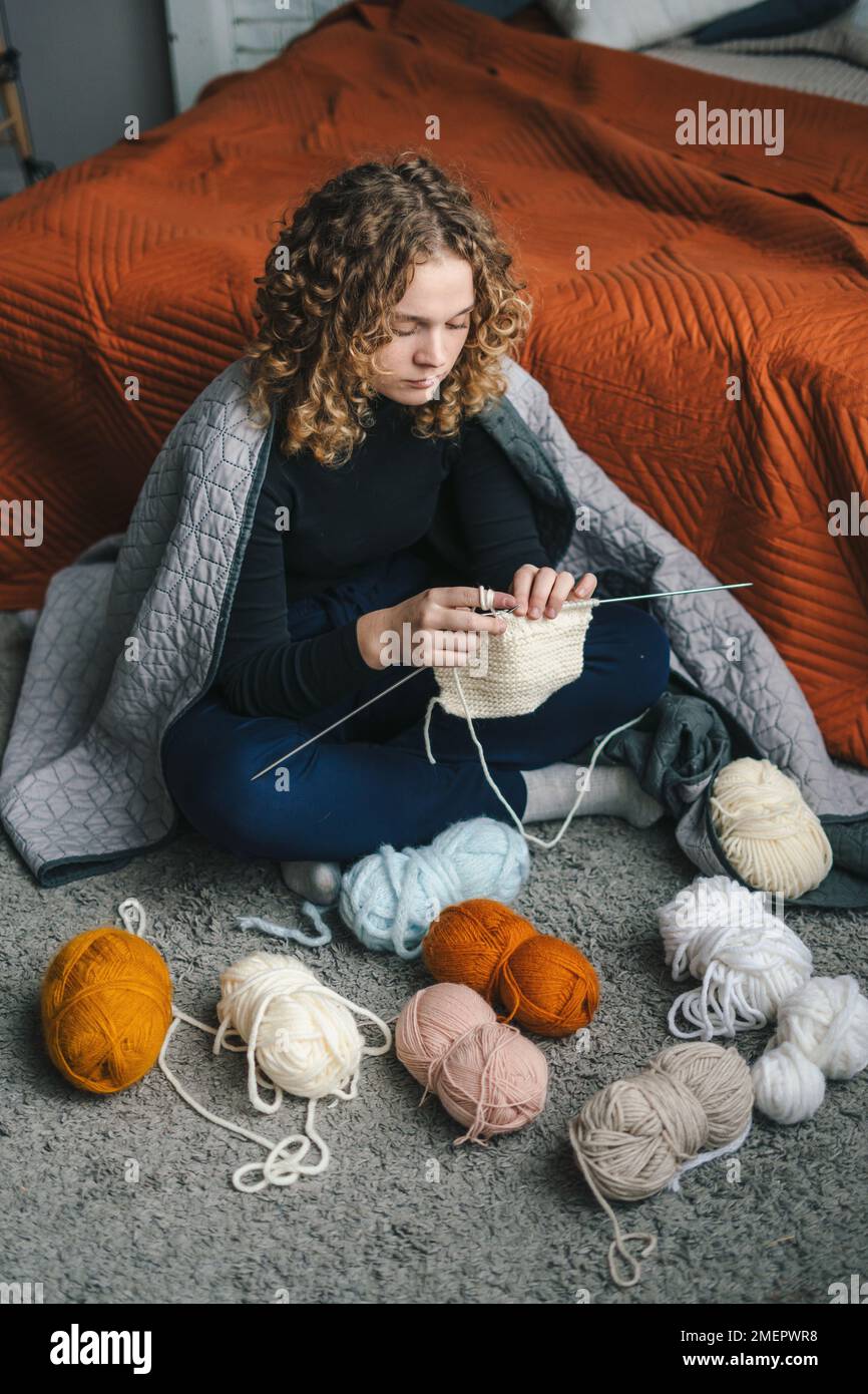 Scene portrait of curly-haired young woman doing knit work at home ...