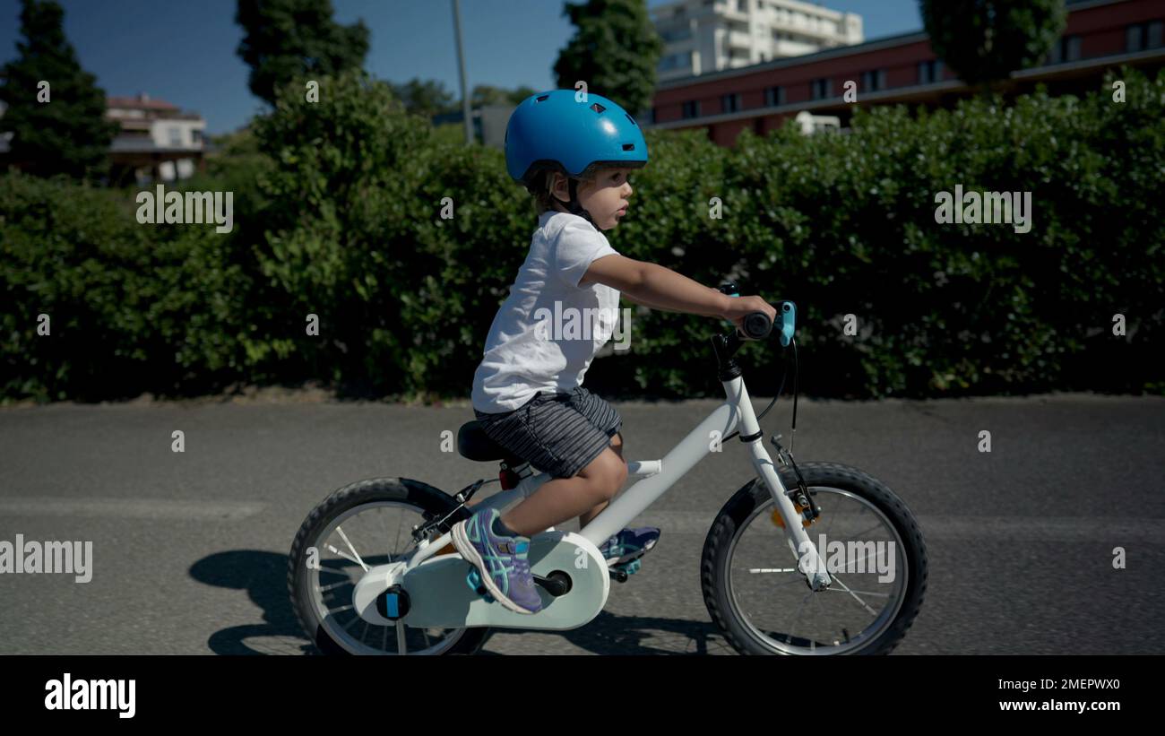 Active little boy rides bicycle outside wearing helmet on green road ...