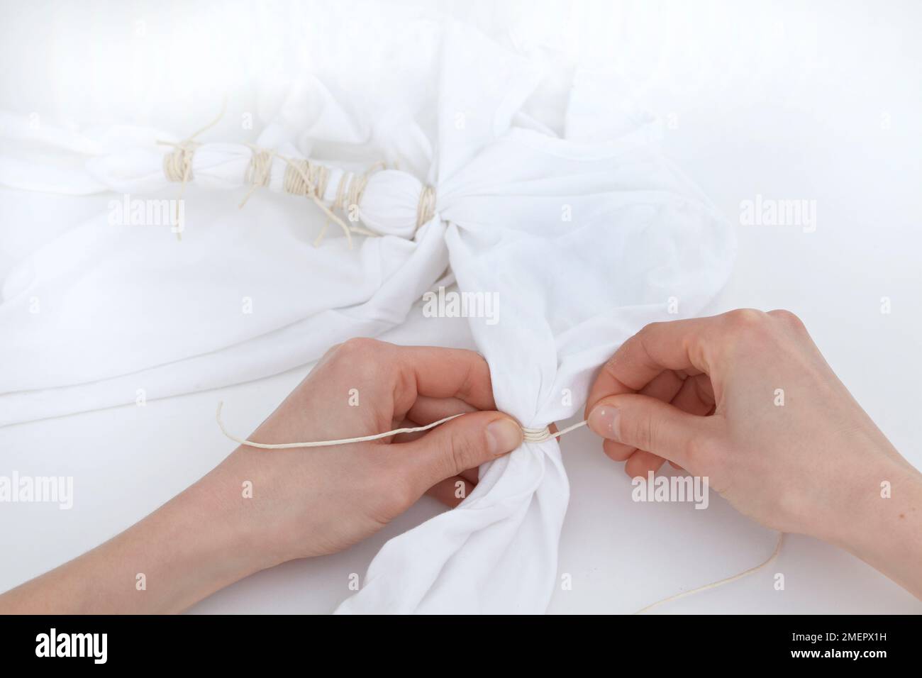 Binding fabric with lengths of string to make tie-dyed T-shirt, close ...