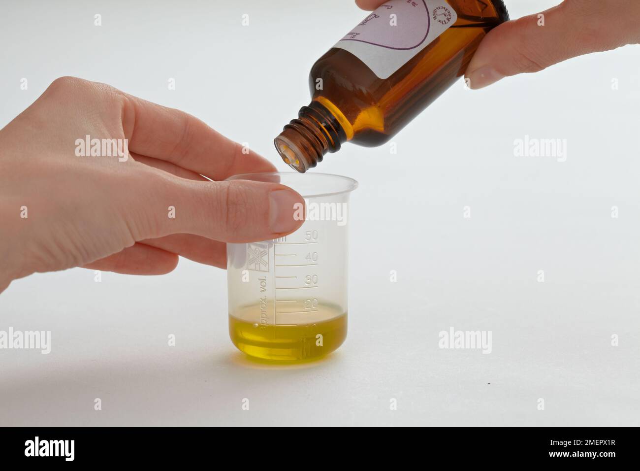Measuring fragrance poured from bottle into small measuring beaker ...