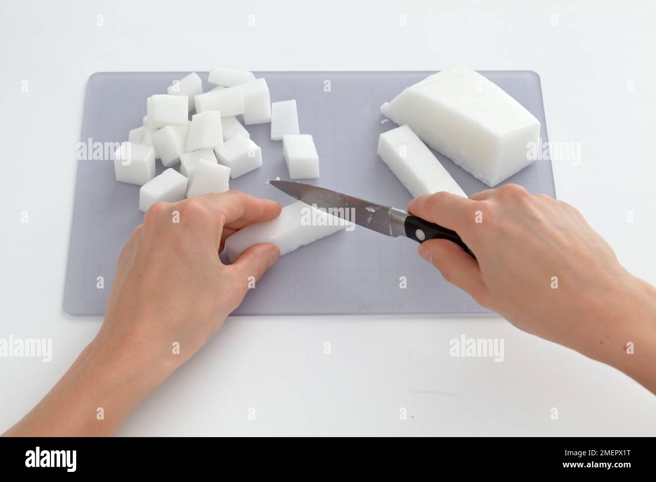Using sharp knife on cutting mat to slice opaque soap base into chunks ...