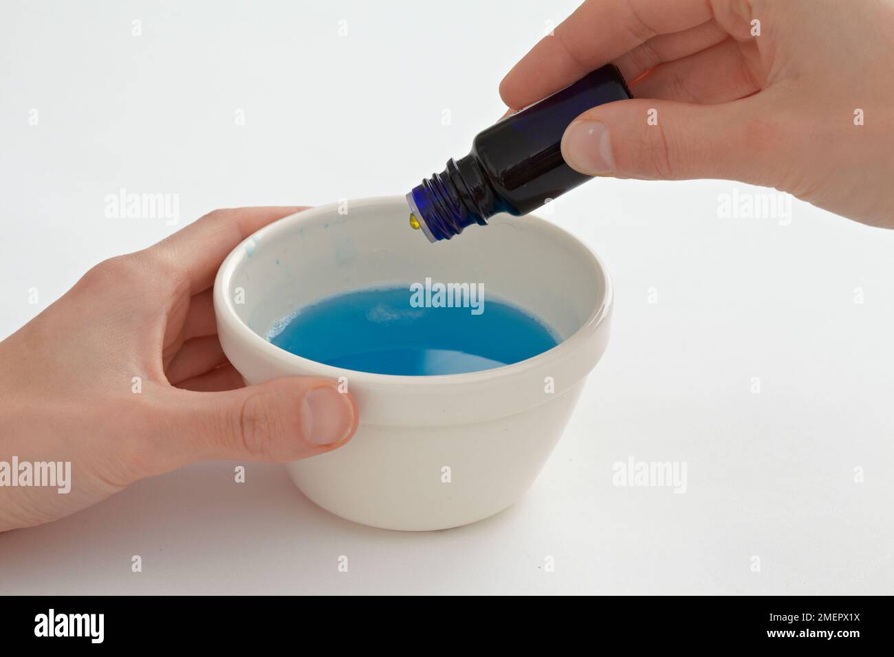 Adding essential oil from small bottle to melted blue soap in small ...