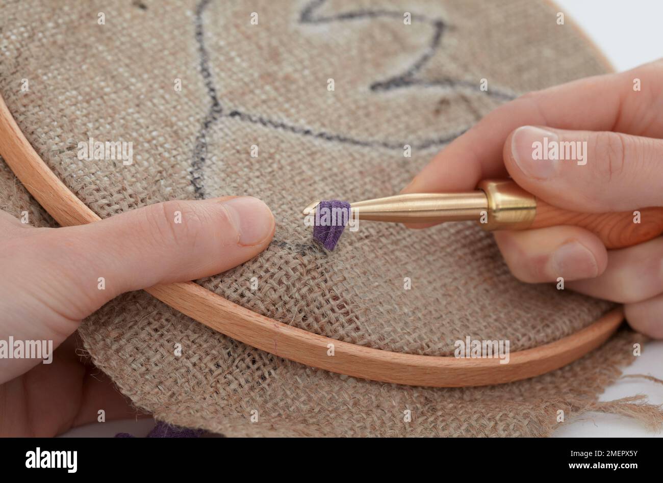 Pulling end of fabric through hessian in embroidery hoop using hook to ...
