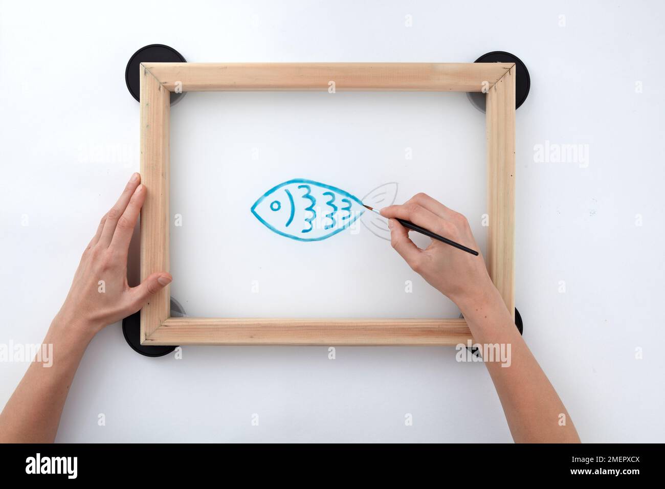 Using paintbrush to go over lines of fish shape on silkscreen, overhead ...