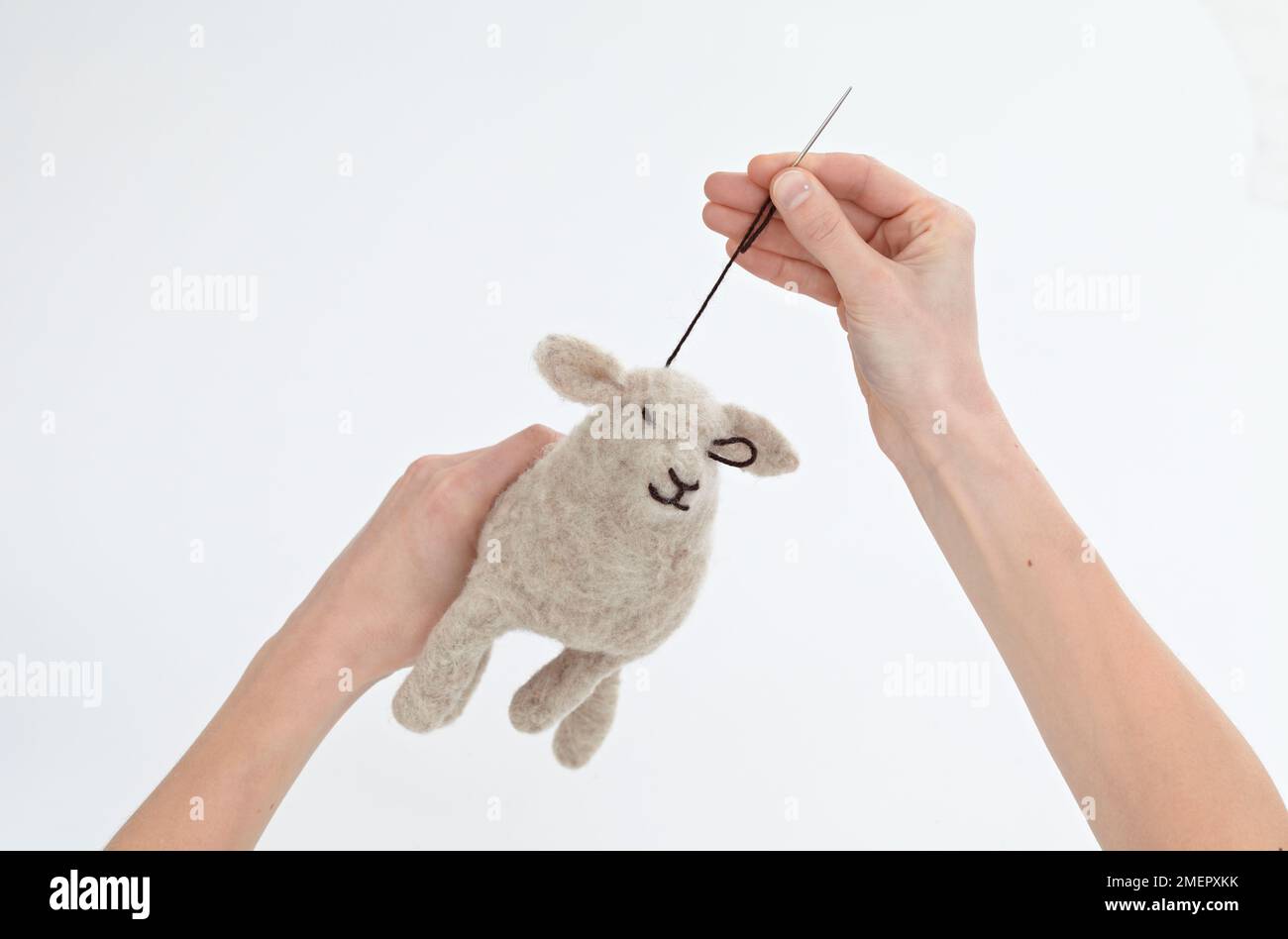 Stitching features of needle-felted sheep using dark brown yarn, close ...