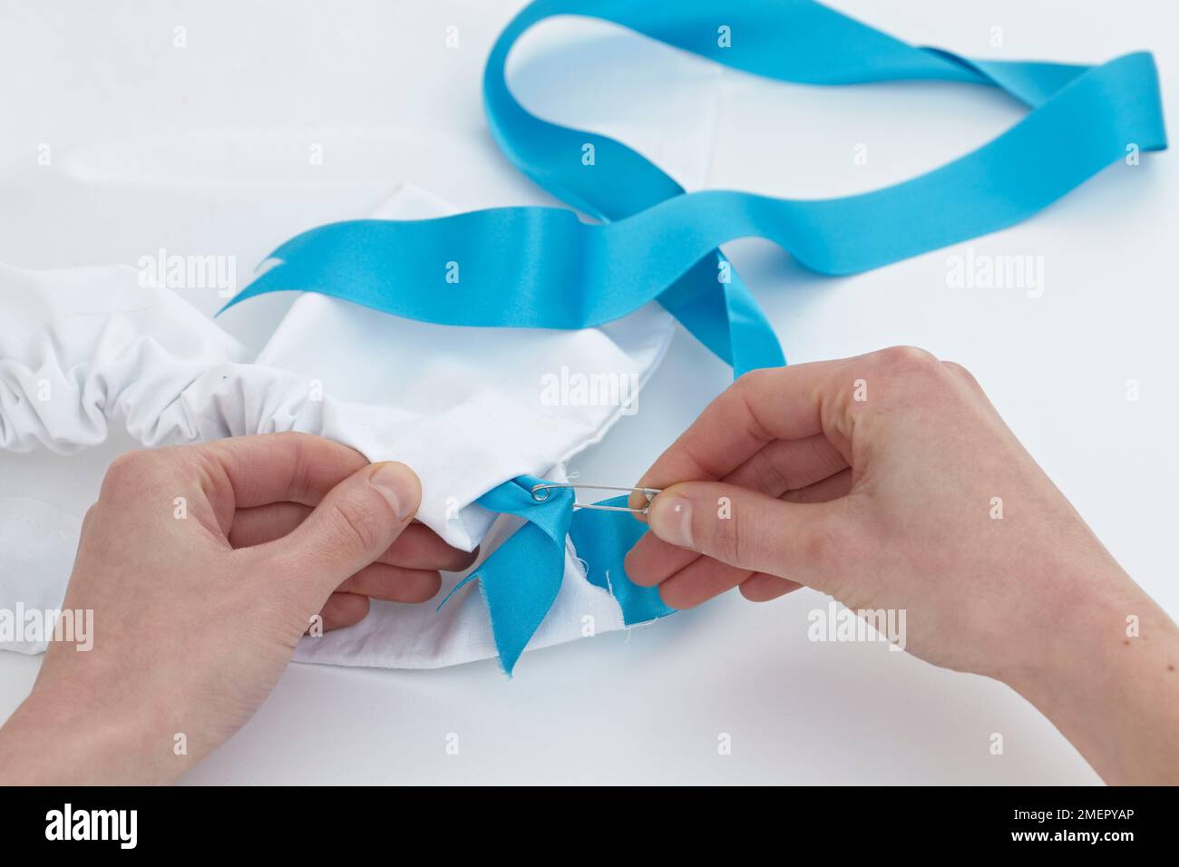Feeding blue ribbon through casing of shoe bag using safety pin, close ...