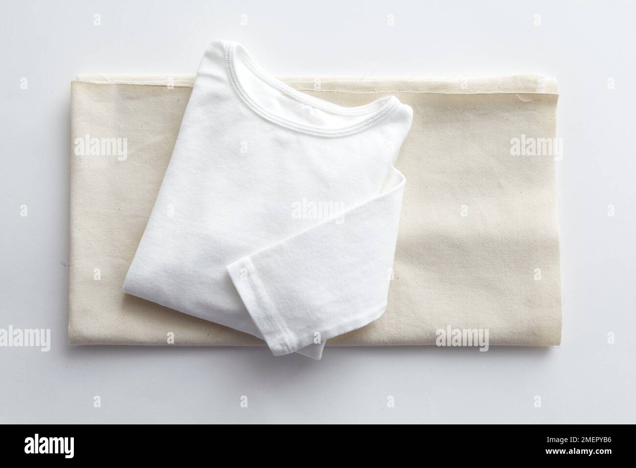 Folded white long sleeved top on top of folded fabric, elevated view ...