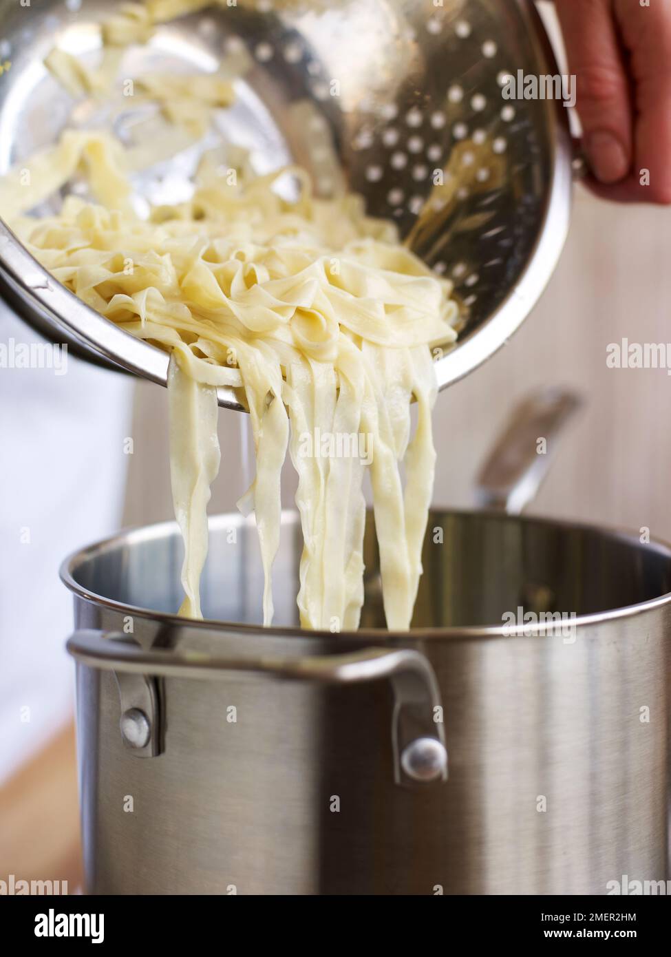 Tipping tagliatelle pasta from colander back into pan Stock Photo - Alamy