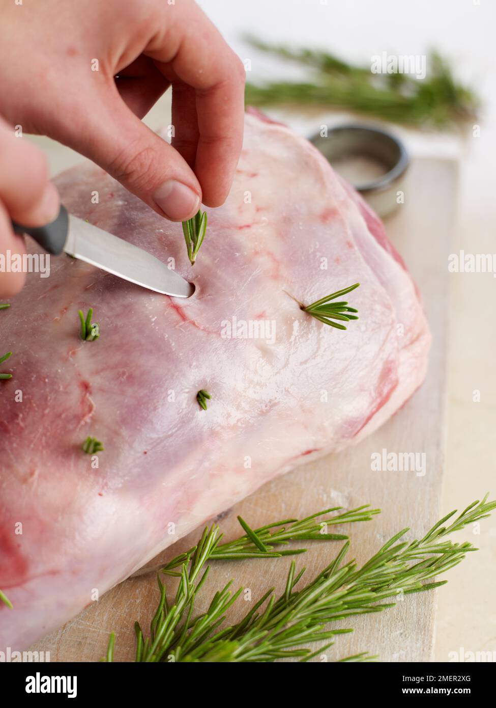 Studding leg of lamb with rosemary, using tip of knife to insert sprigs ...