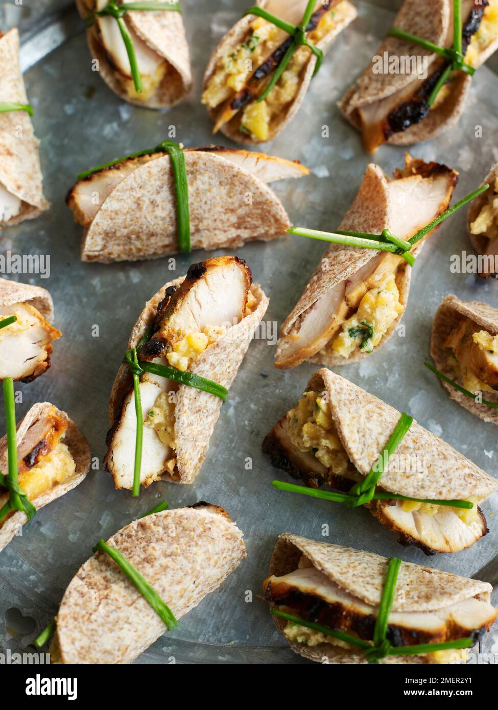 Tandoori chicken and peach chutney bites, tied with chive stalks Stock ...