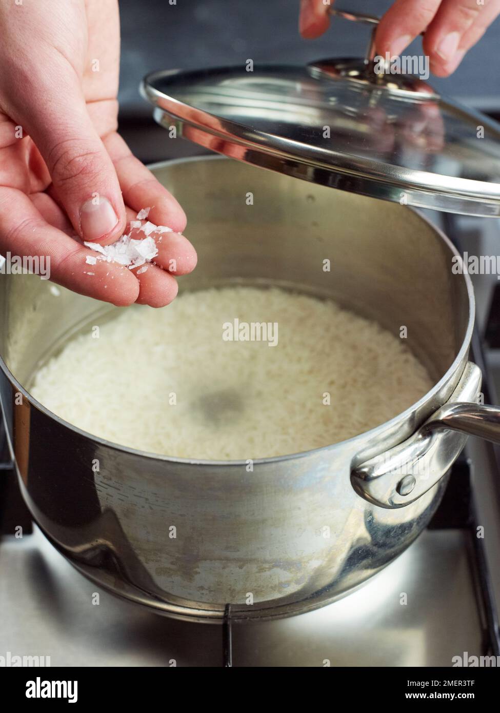Adding salt to pan containing rice and twice the amount of cold water ...